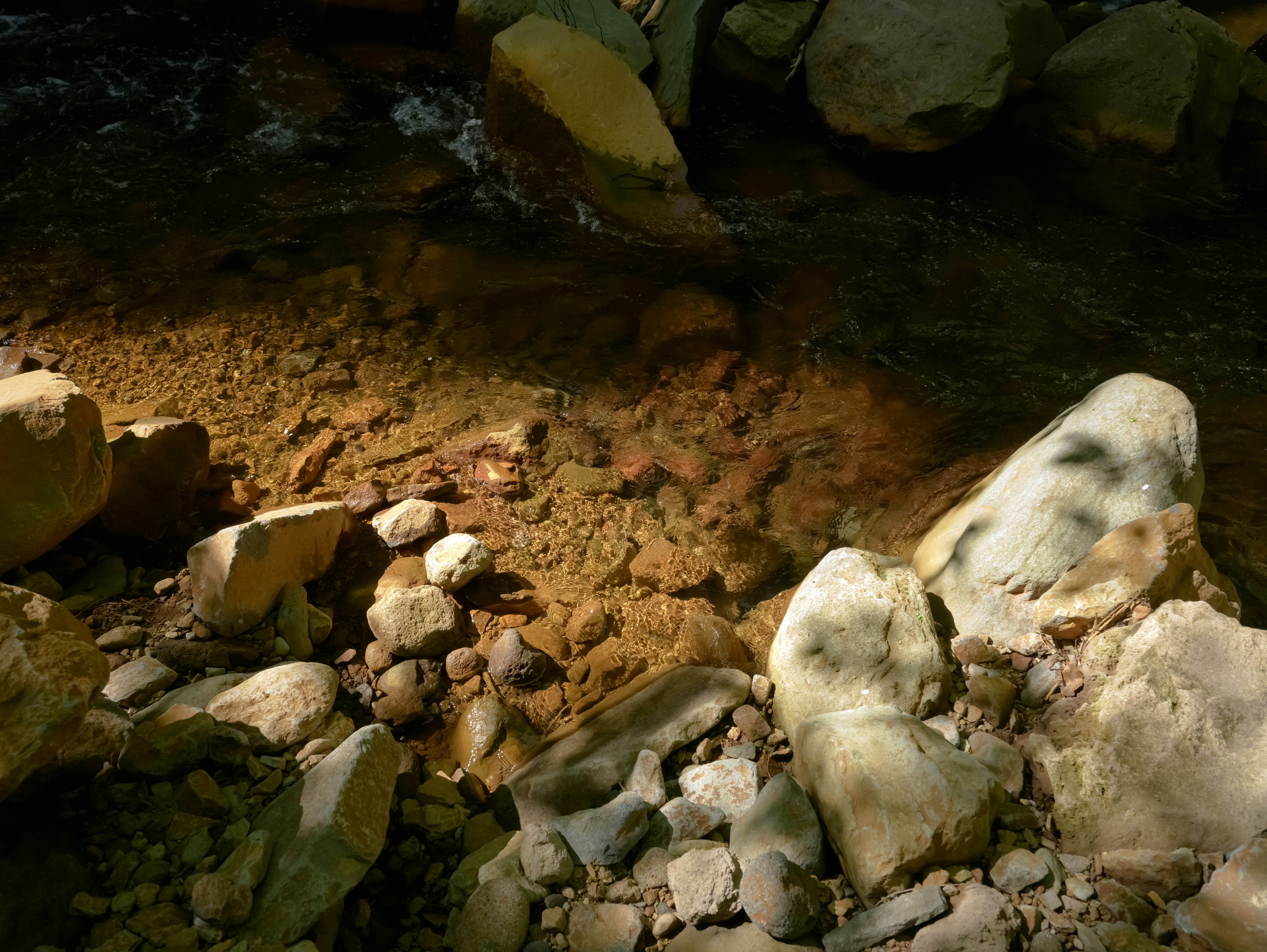 Stones and rocks surround a brown, sandy riverbank. photo – Free Rock ...
