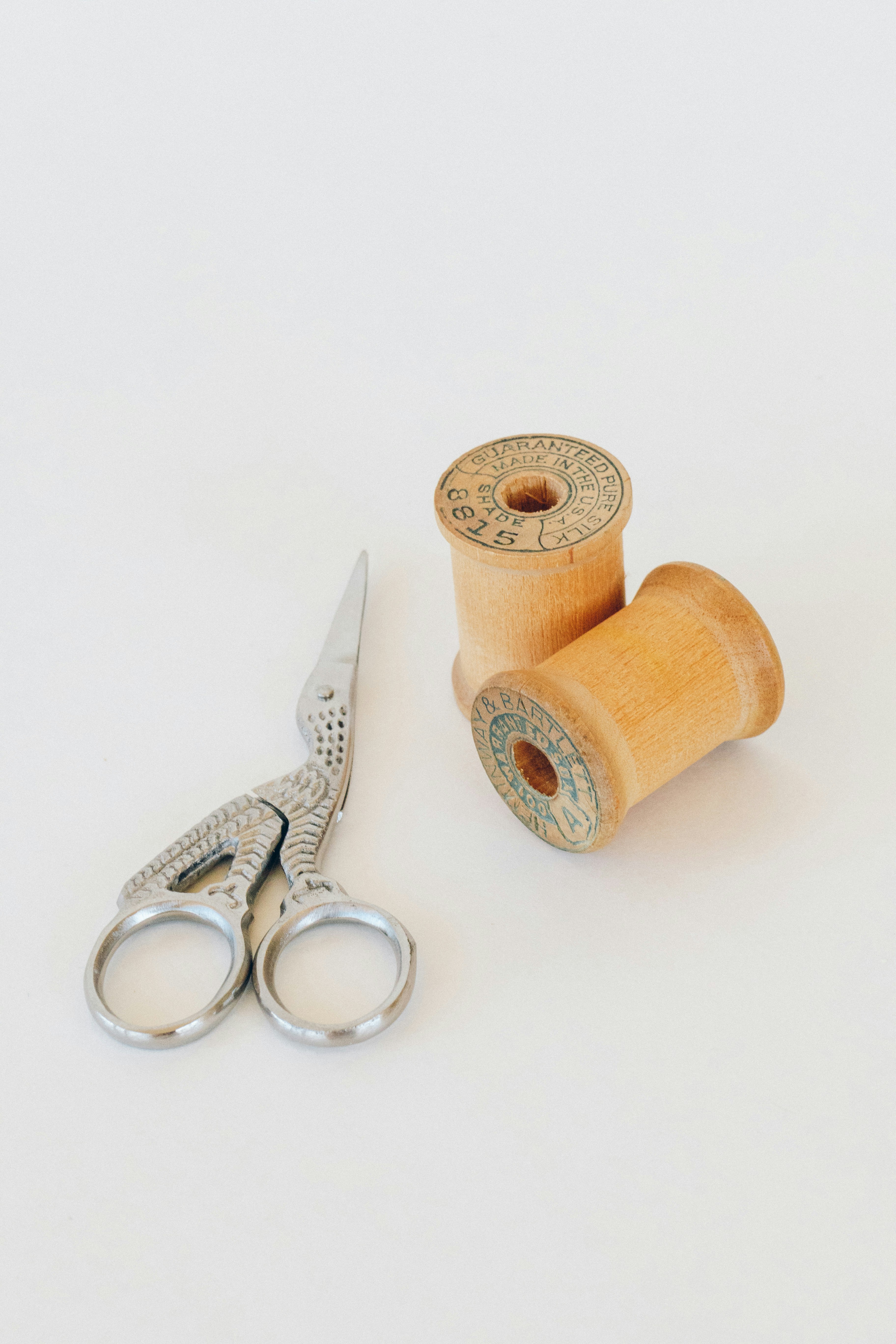 Crafting scisors and wooden thread spools | Scissors and spools rest on a white background.