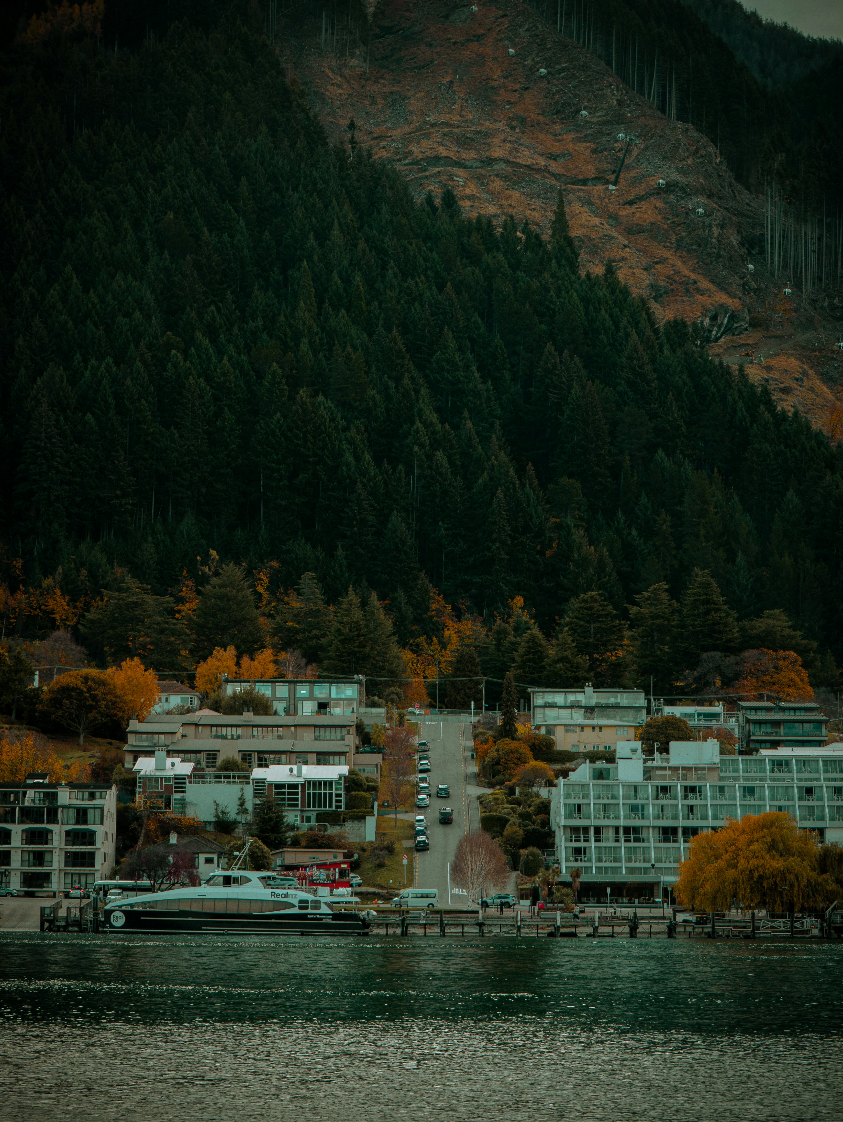 Colorful autumn foliage frames a tranquil waterfront scene, showcasing a blend of residential architecture and boats along the shore. 
