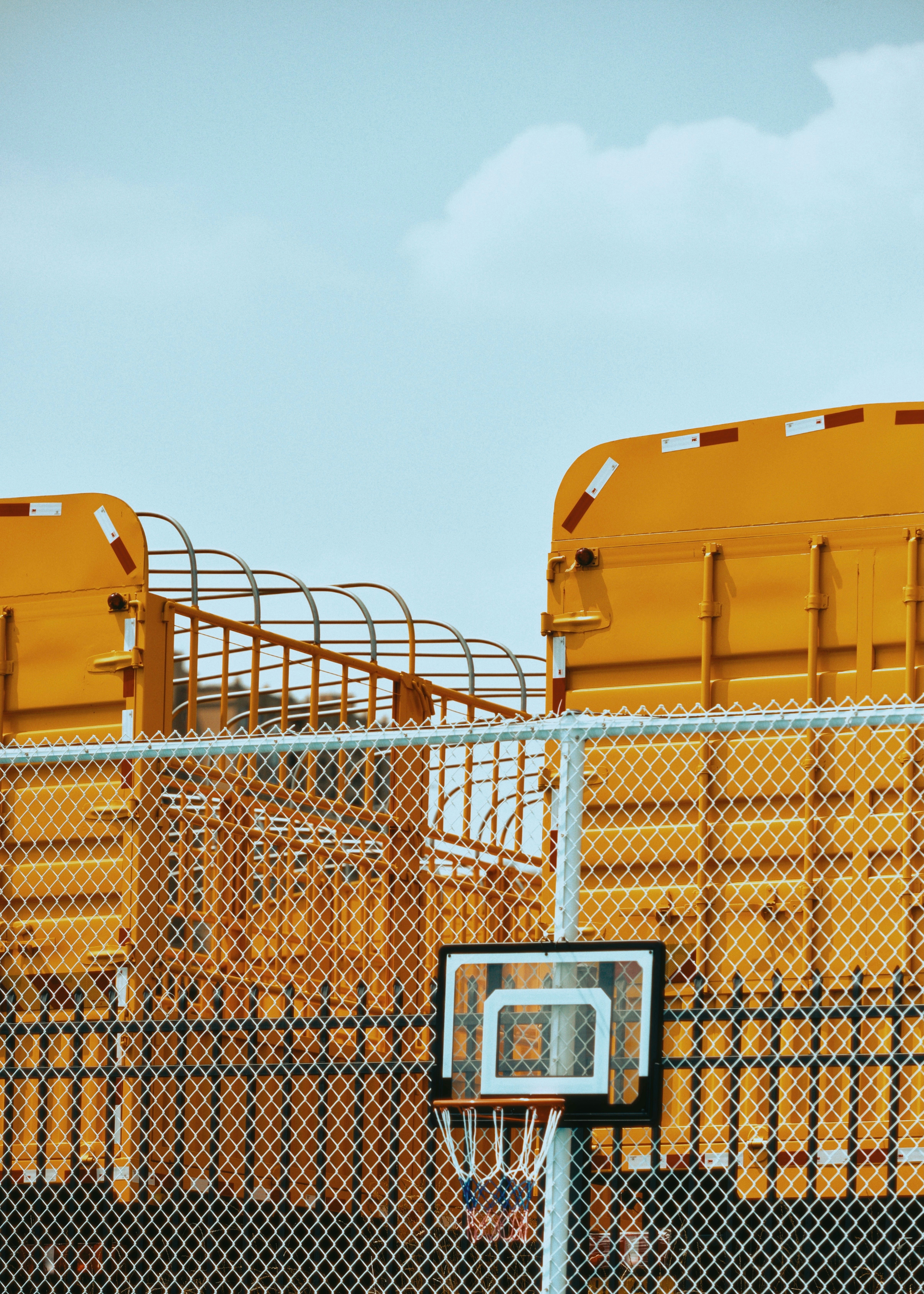 A basketball hoop stands in front of yellow trains.