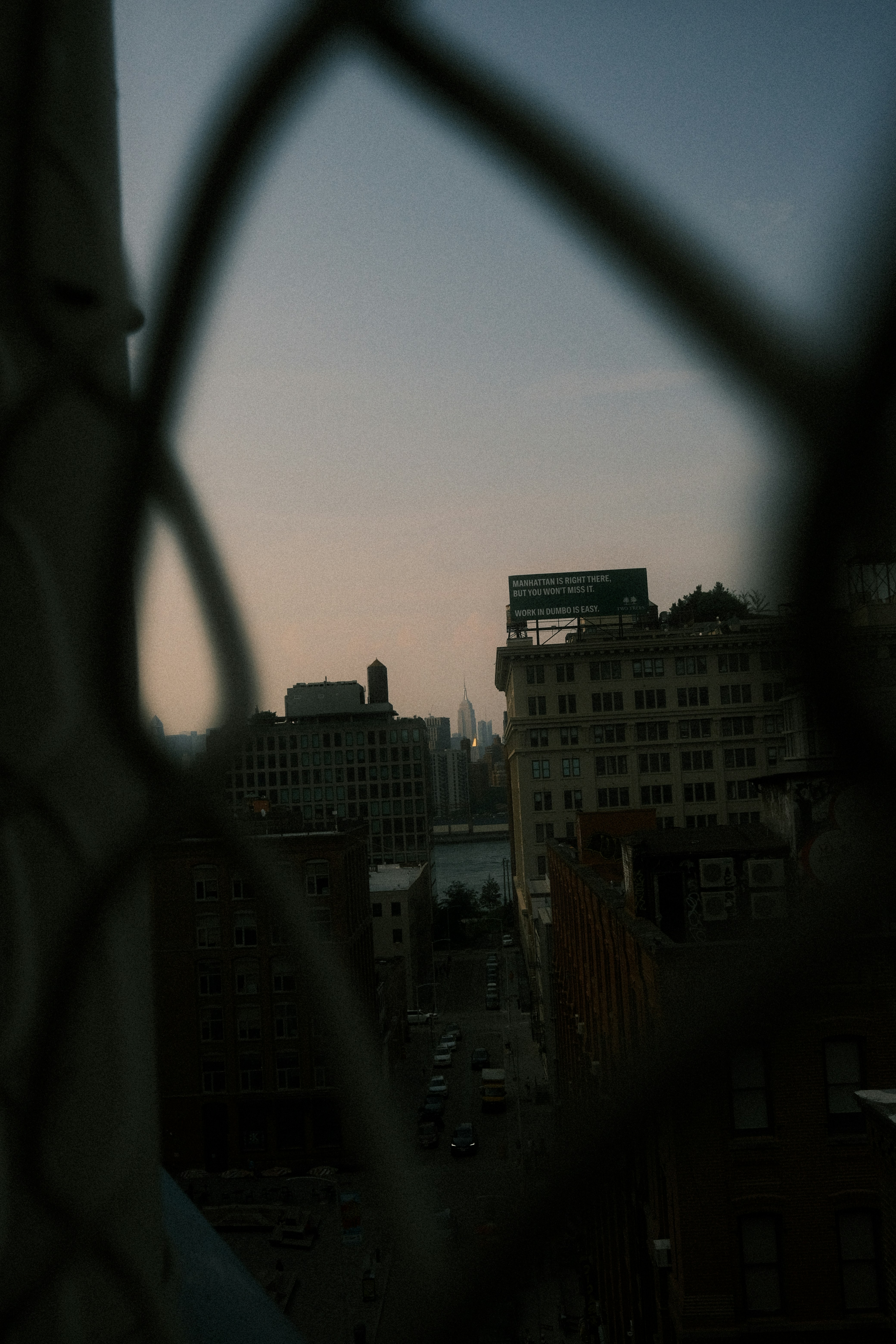 City skyline viewed through a chain-link fence.