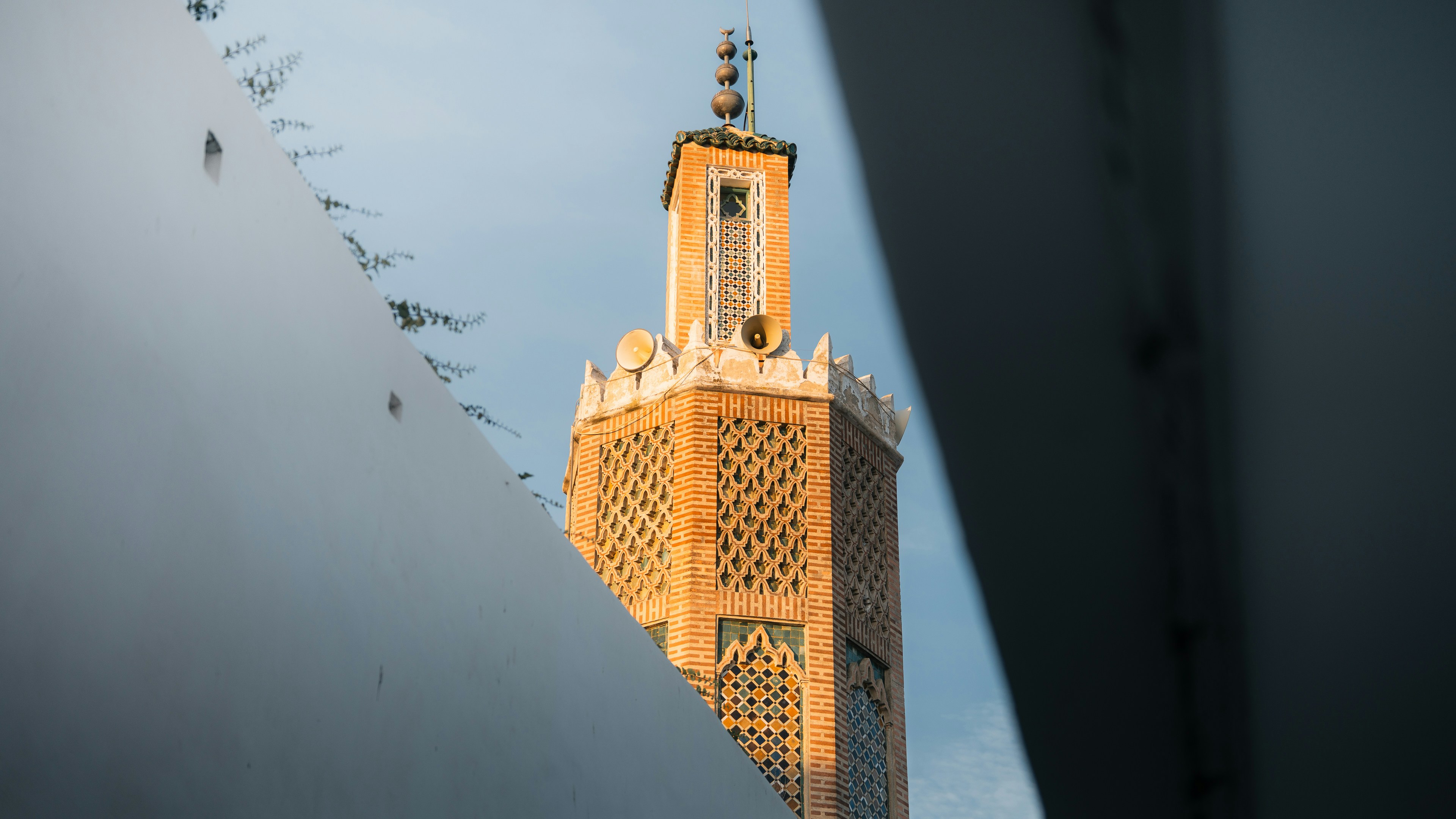 Intricate minaret rises against a soft sky, framed by modern architectural lines. The warm light accentuates its ornate details.