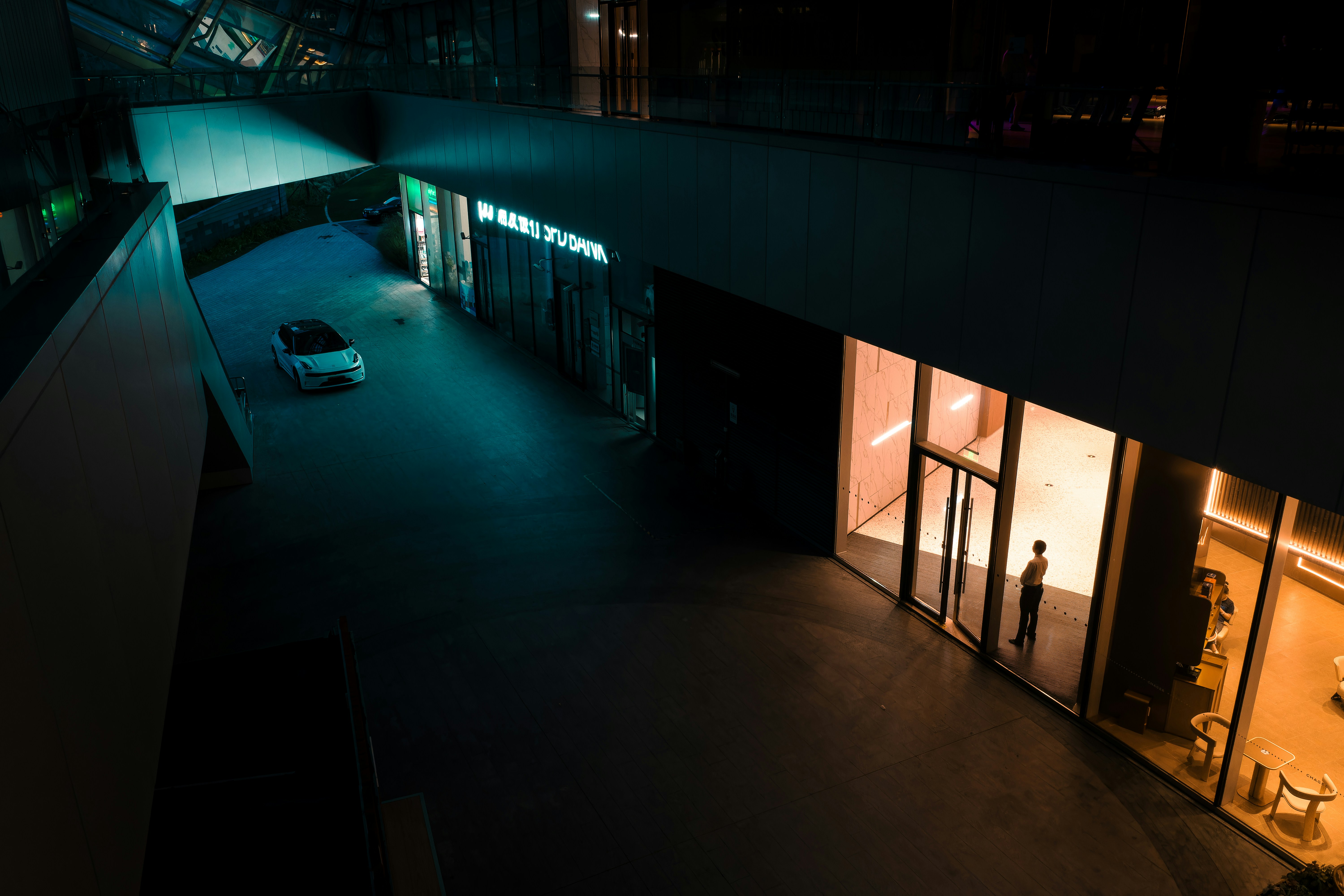 A serene urban scene showcasing contrasting lighting in a modern architectural space, with a lone figure framed by illuminated glass doors. 
