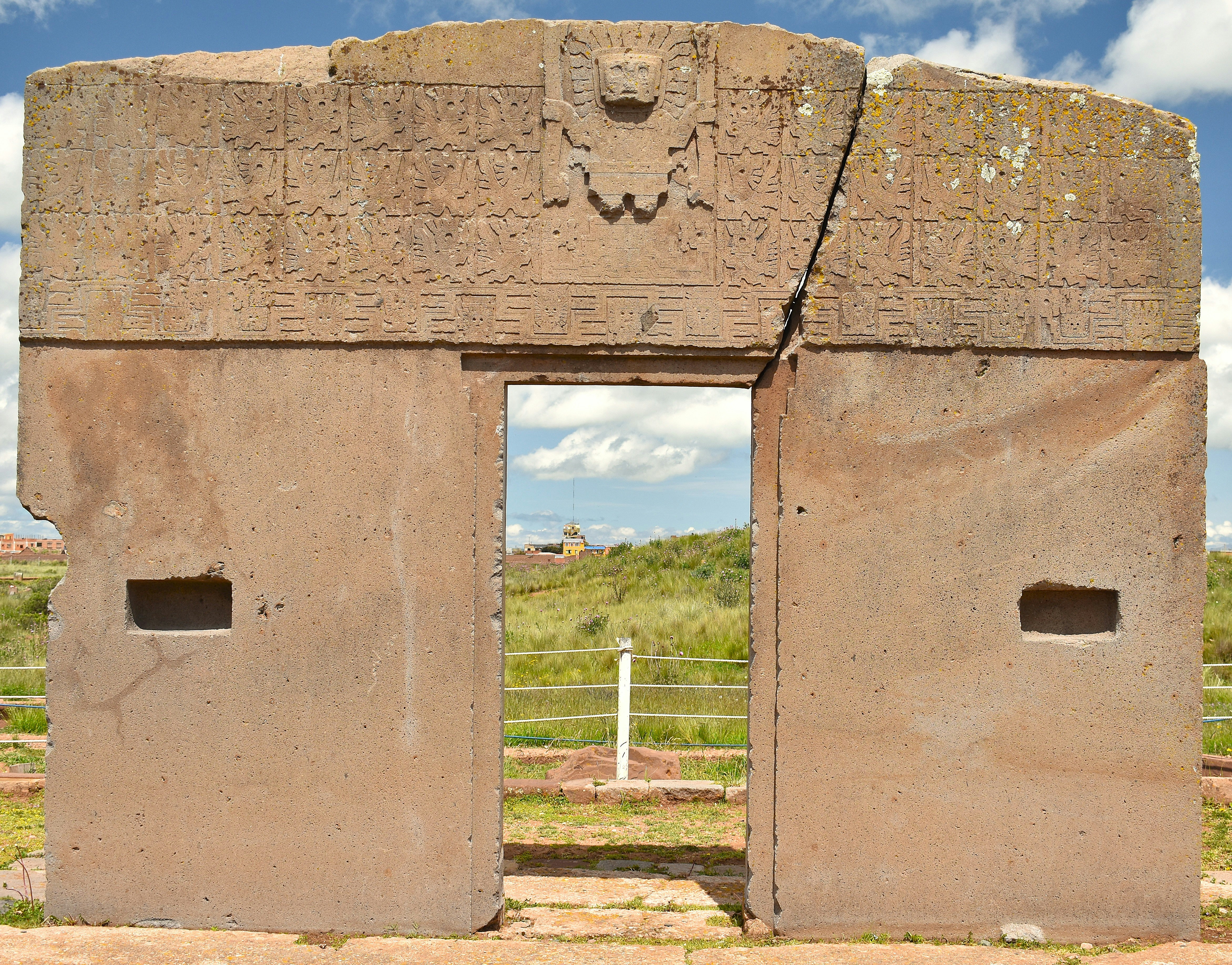 Intricate stone doorway with carvings, framed by a lush green landscape under a blue sky.