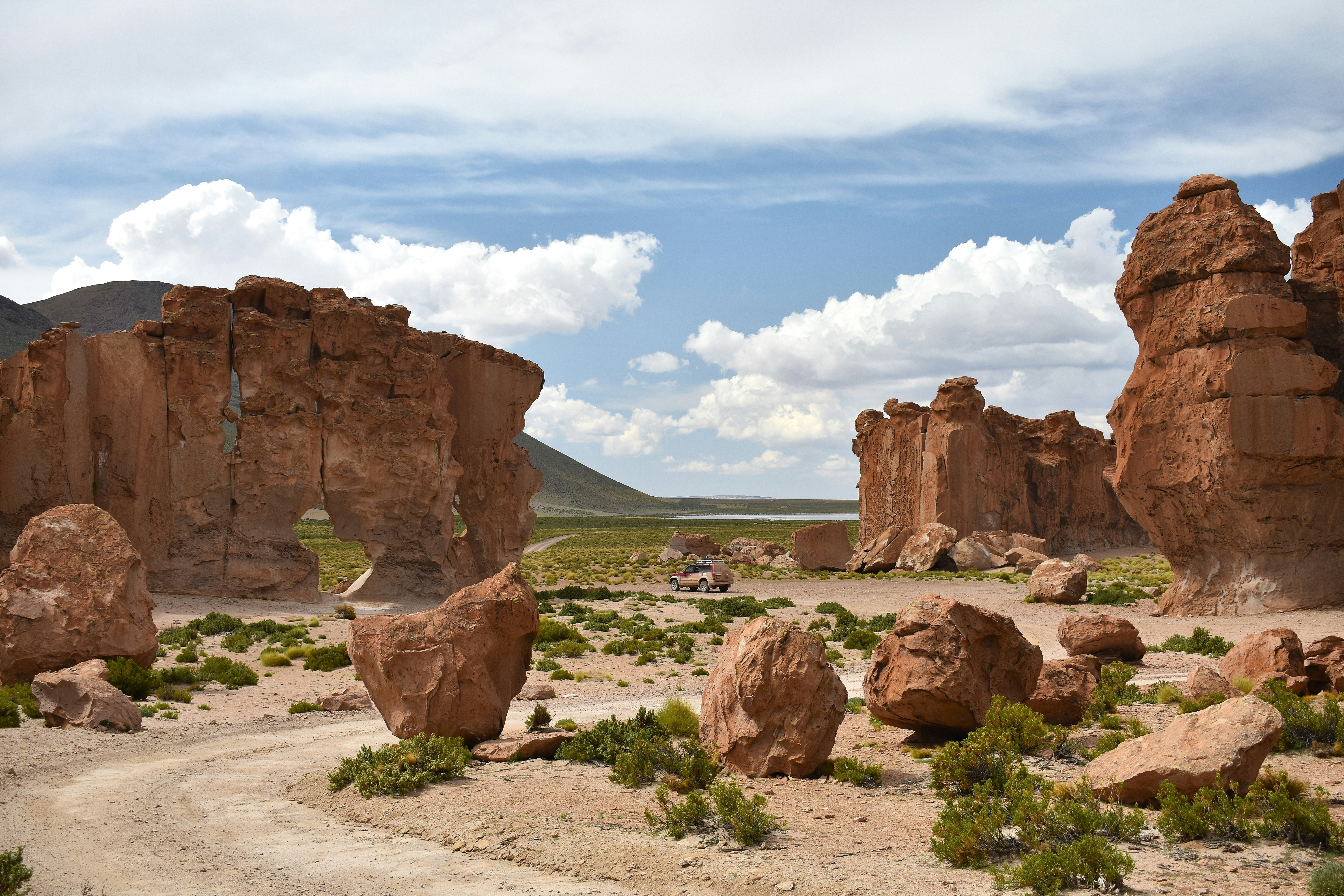 Massive rock formations rise majestically against a backdrop of clouds and distant mountains in a remote landscape.