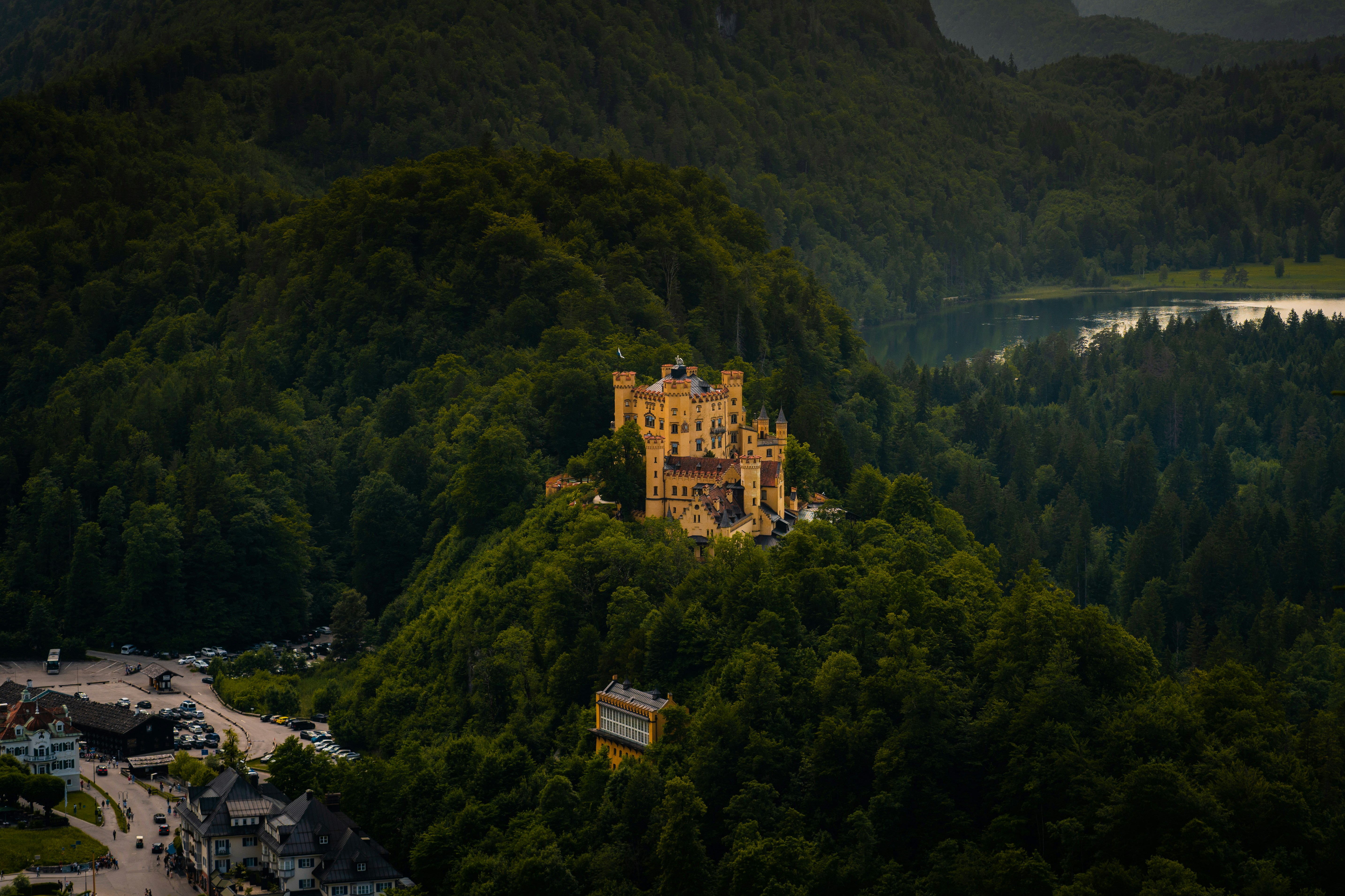 A majestic yellow castle perched atop a lush green hill, surrounded by dense forest and a serene lake in the background.