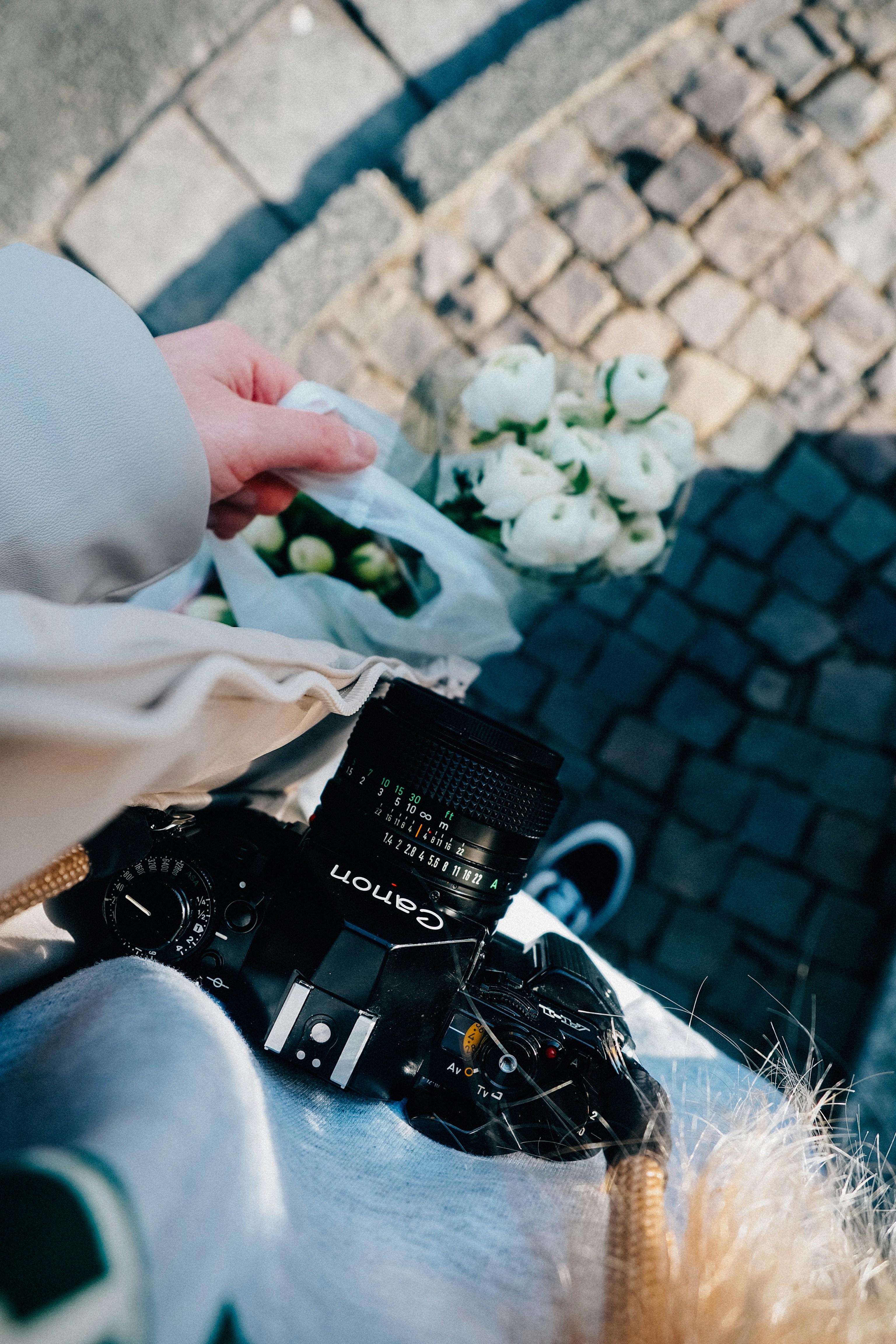 A camera sits with flowers in someone's hand.
