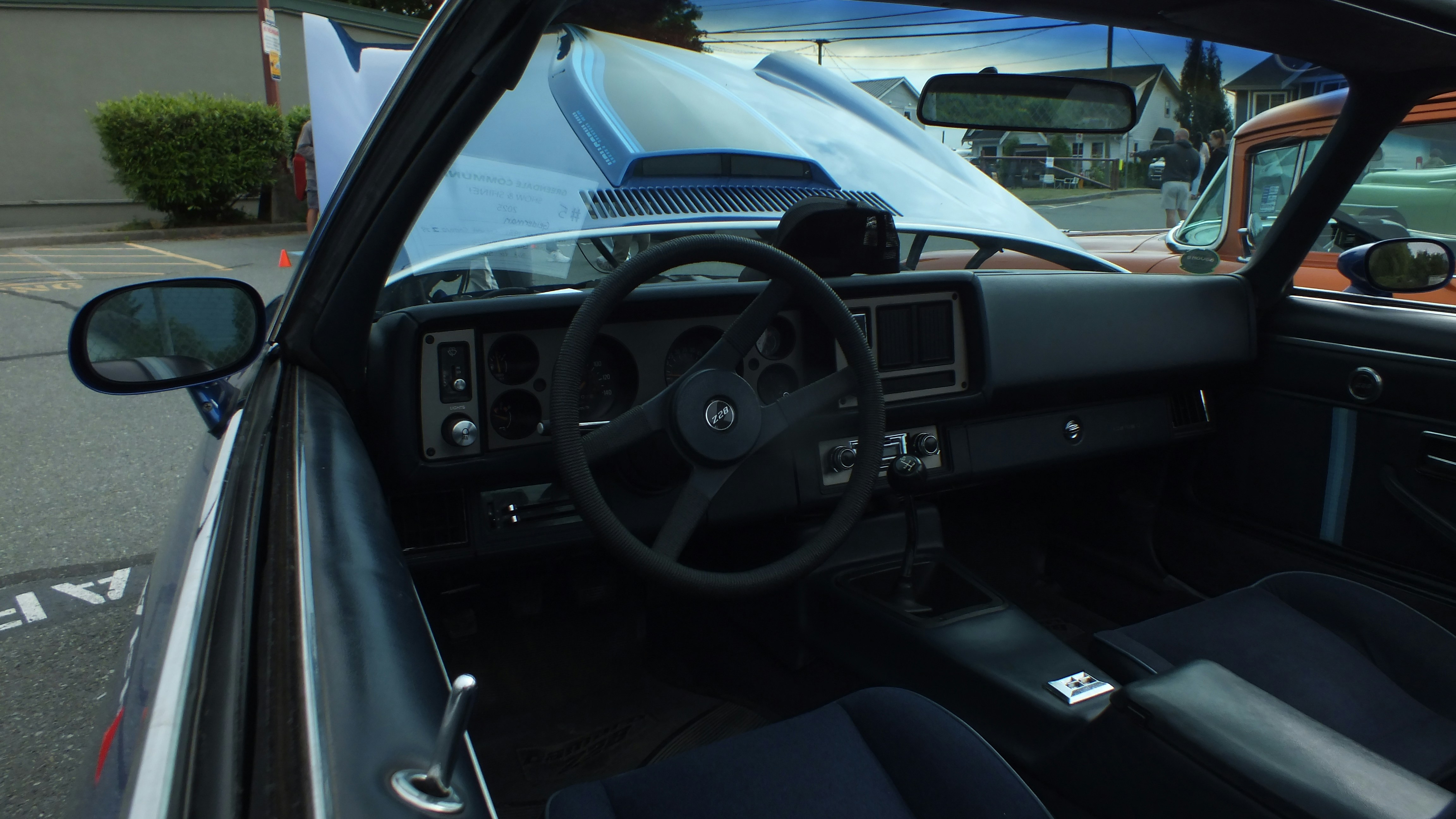 Interior view of a vintage car showcasing the steering wheel and dashboard details. The hood is open, revealing the engine compartment.