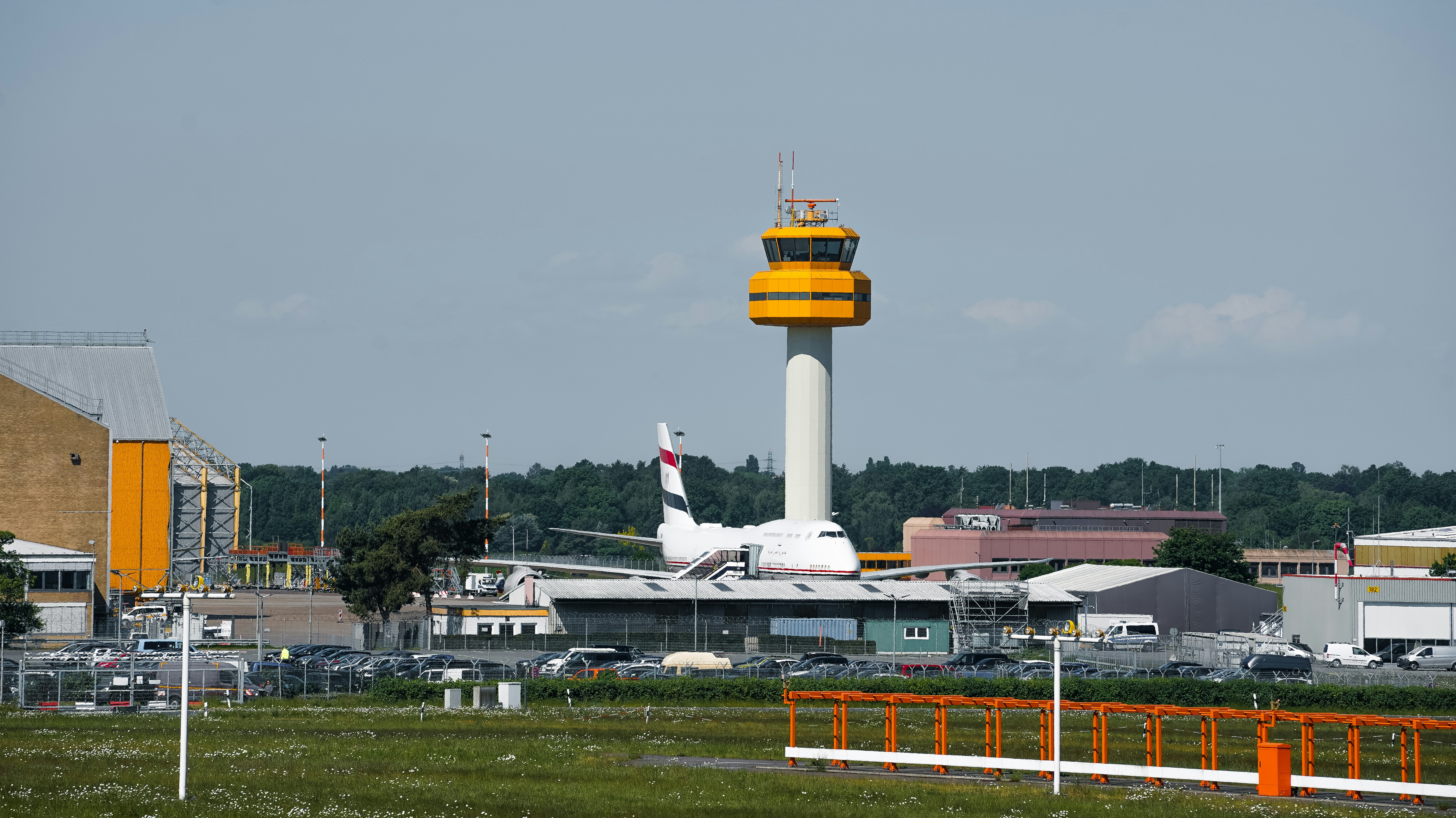 Airplane parked near a distinctive yellow airport control tower under a clear sky.