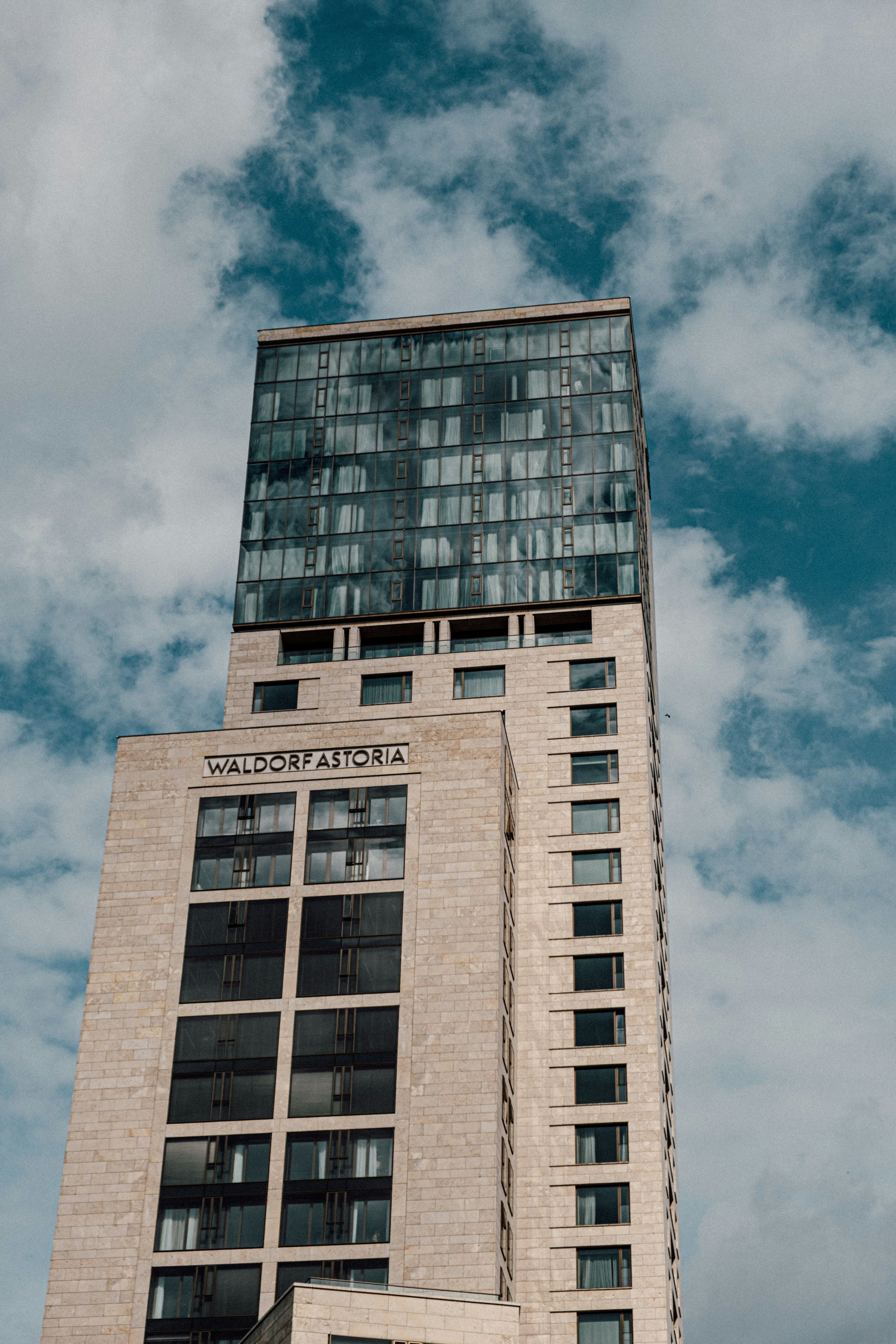 Modern architectural marvel of the Waldorf Astoria hotel against a dynamic sky, showcasing its sleek lines and reflective glass facade.