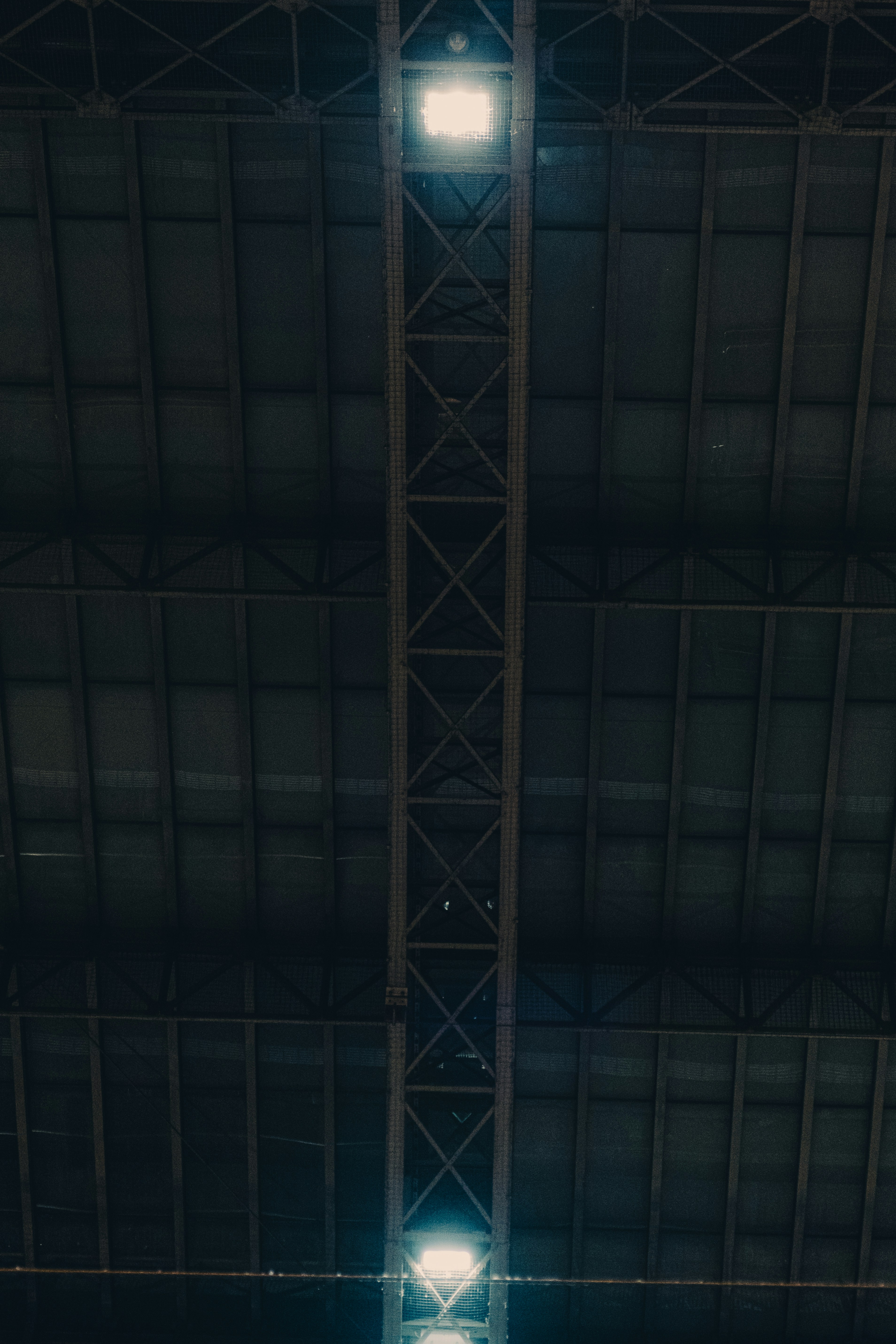 Industrial ceiling with exposed beams and bright overhead lights illuminating the structure's geometry.