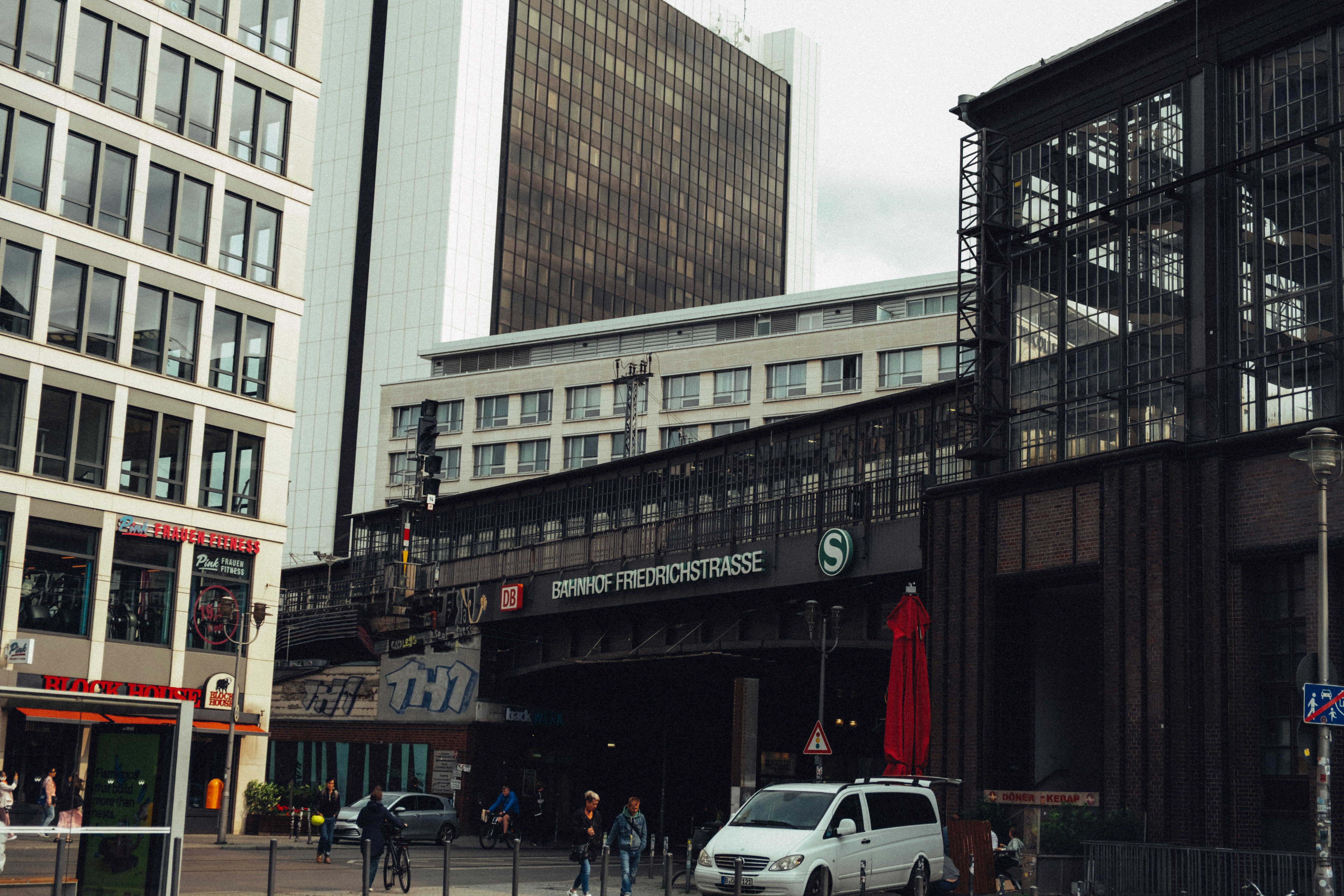 A bustling urban scene showcasing the Friedrichstraße train station amidst contemporary architecture. The juxtaposition highlights the blend of historical and modern design elements.