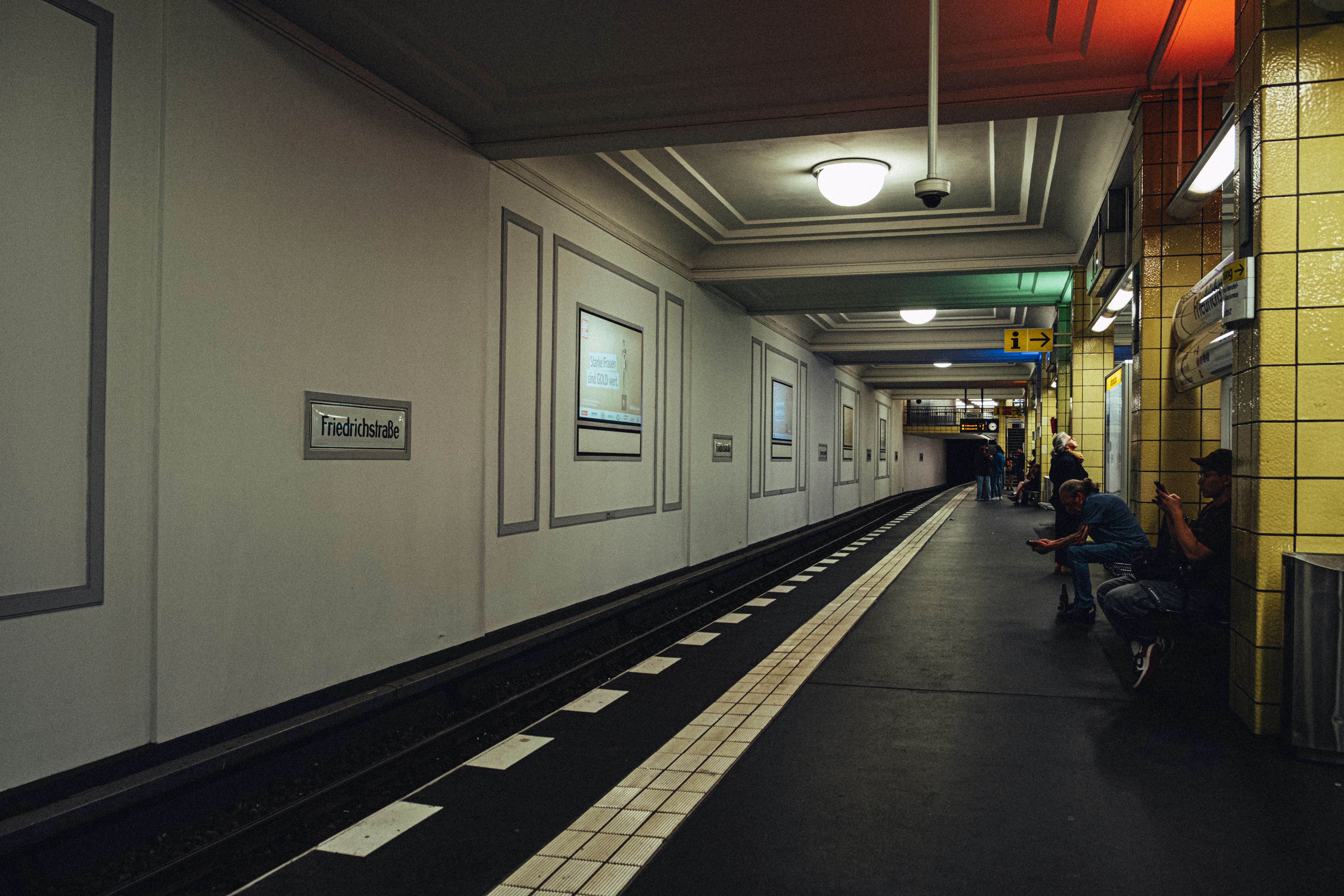Quiet subway platform with minimal passenger activity, showcasing the architectural details of the station. The warm lighting contrasts with the cool tones of the walls.