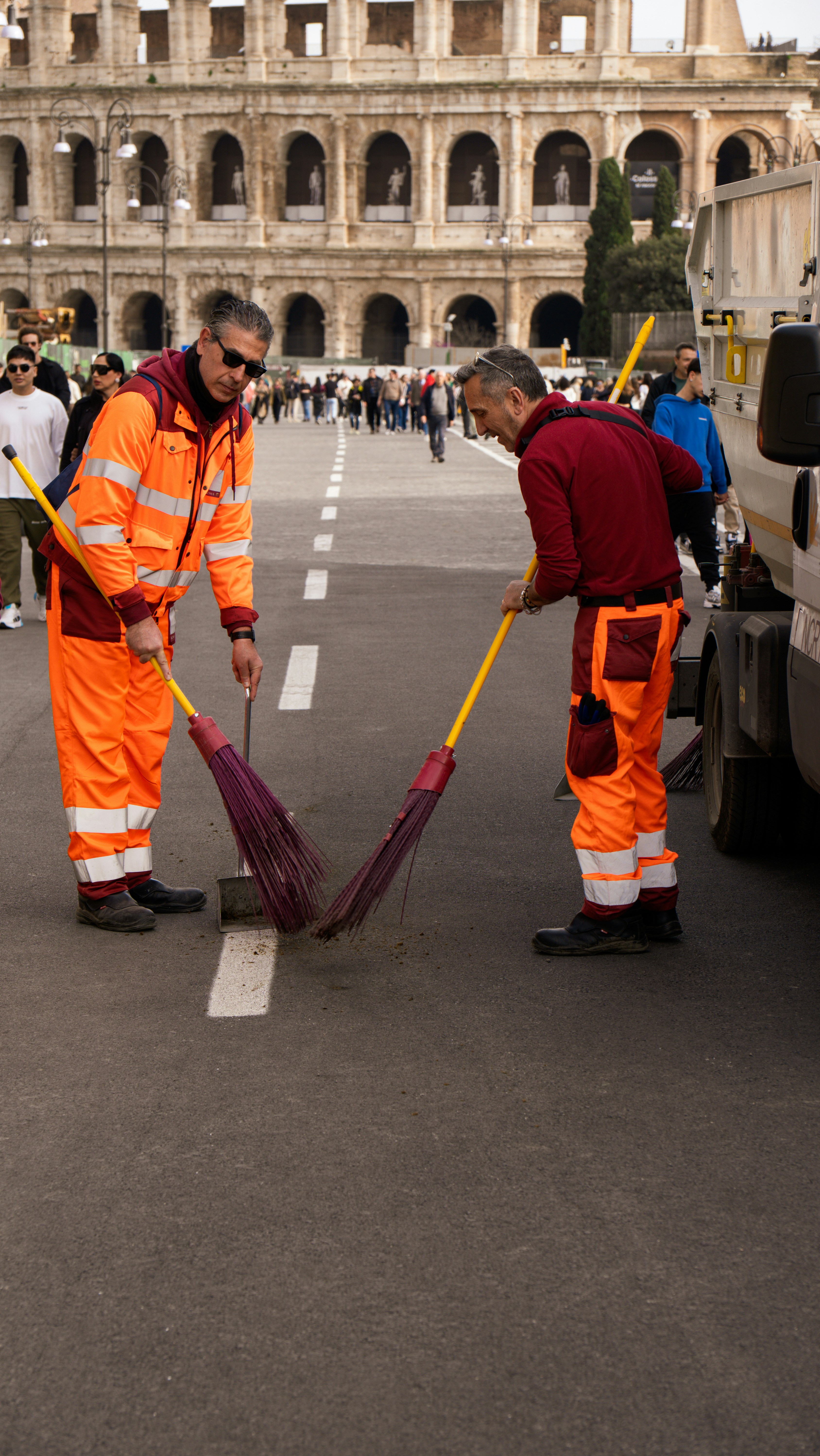 Sweeping in the Colosseum Shadow: Neon-Orange Workers on a Busy Roman Street