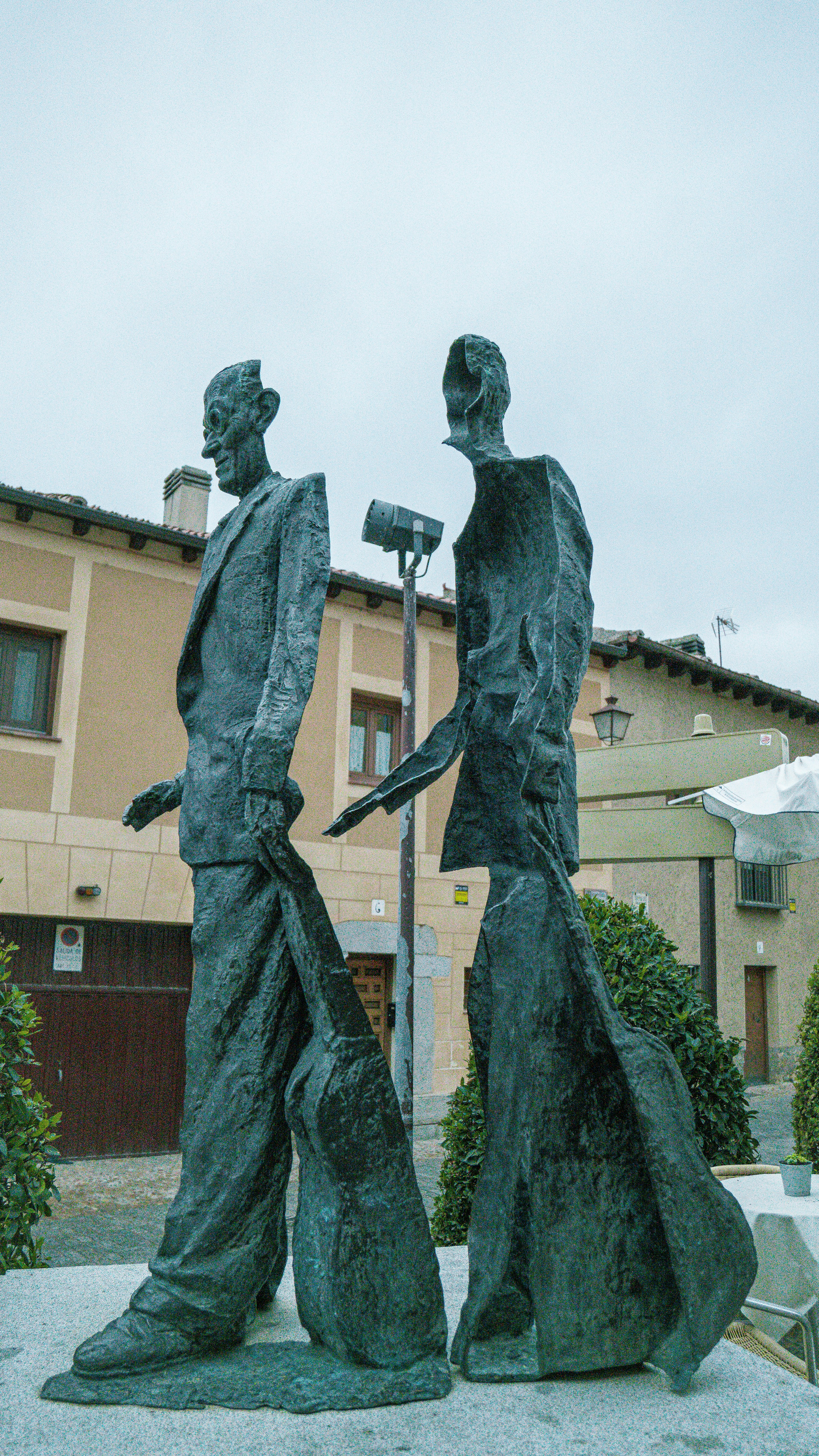 Two Slender Bronze Figures Stride Through a Quiet Piazza