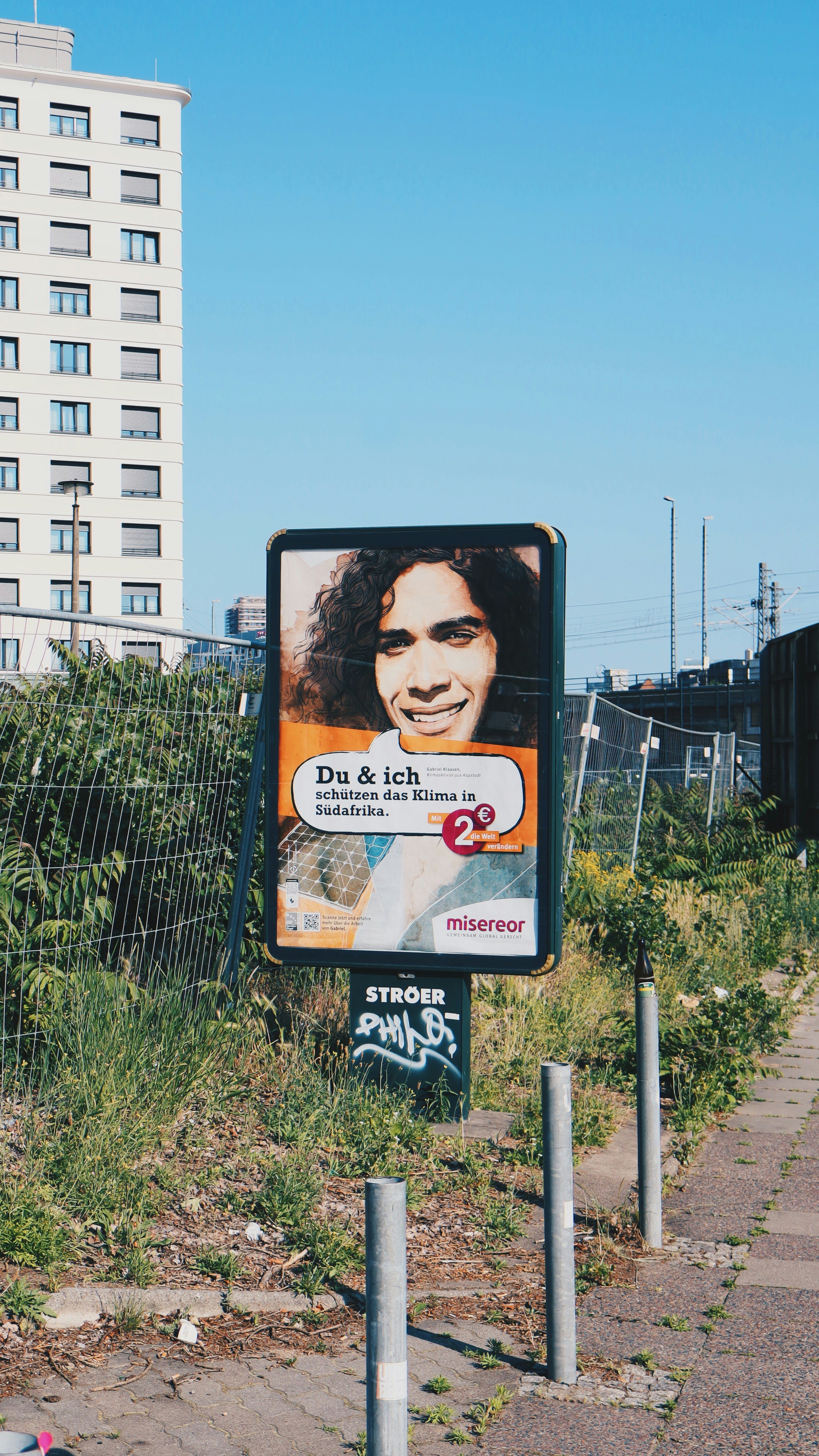 Poster Portrait by the Fence: A Street-Side Message Under a Clear Sky