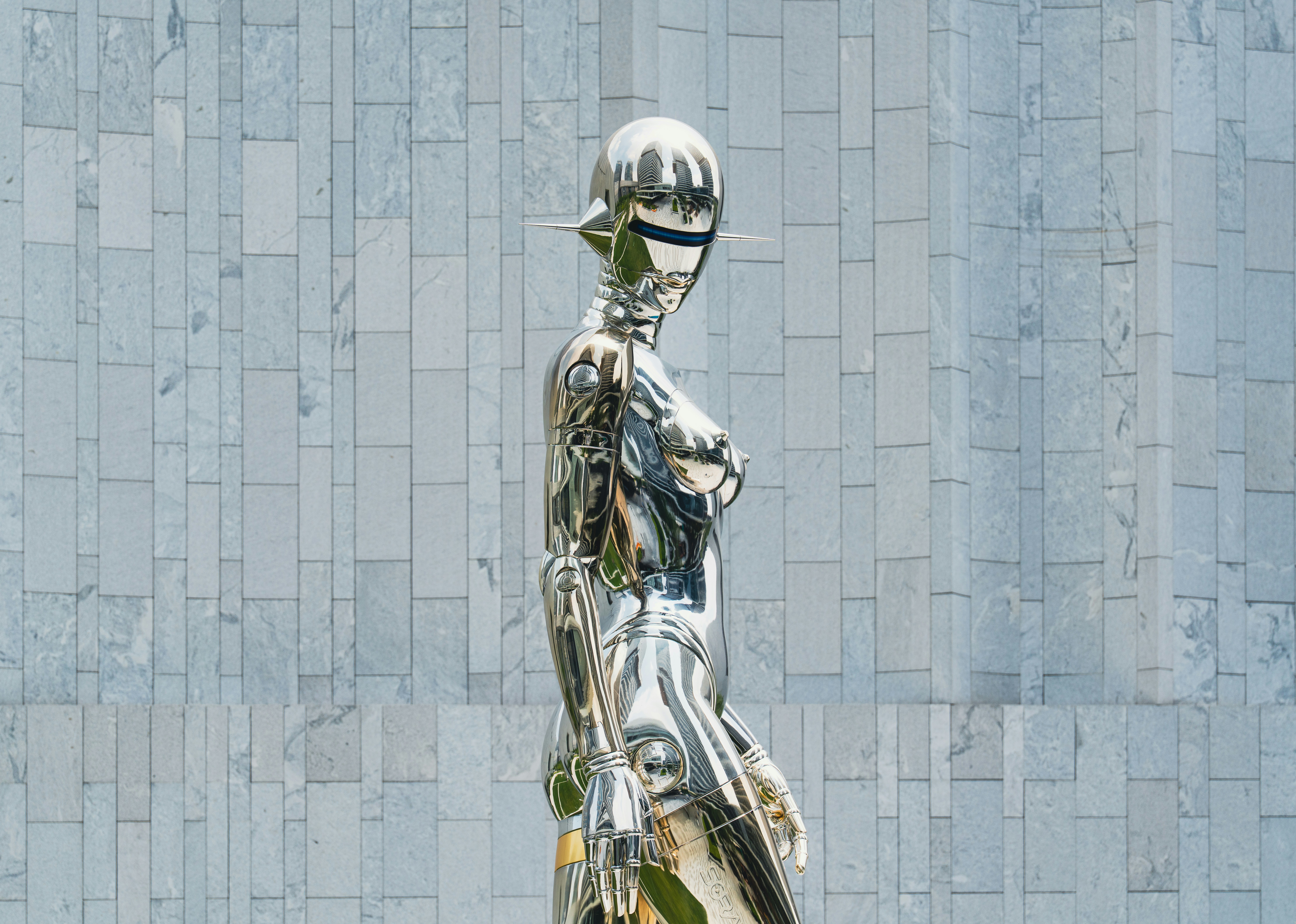 Polished Sentinel: A chrome humanoid sculpture mirrored by a stone-brick wall