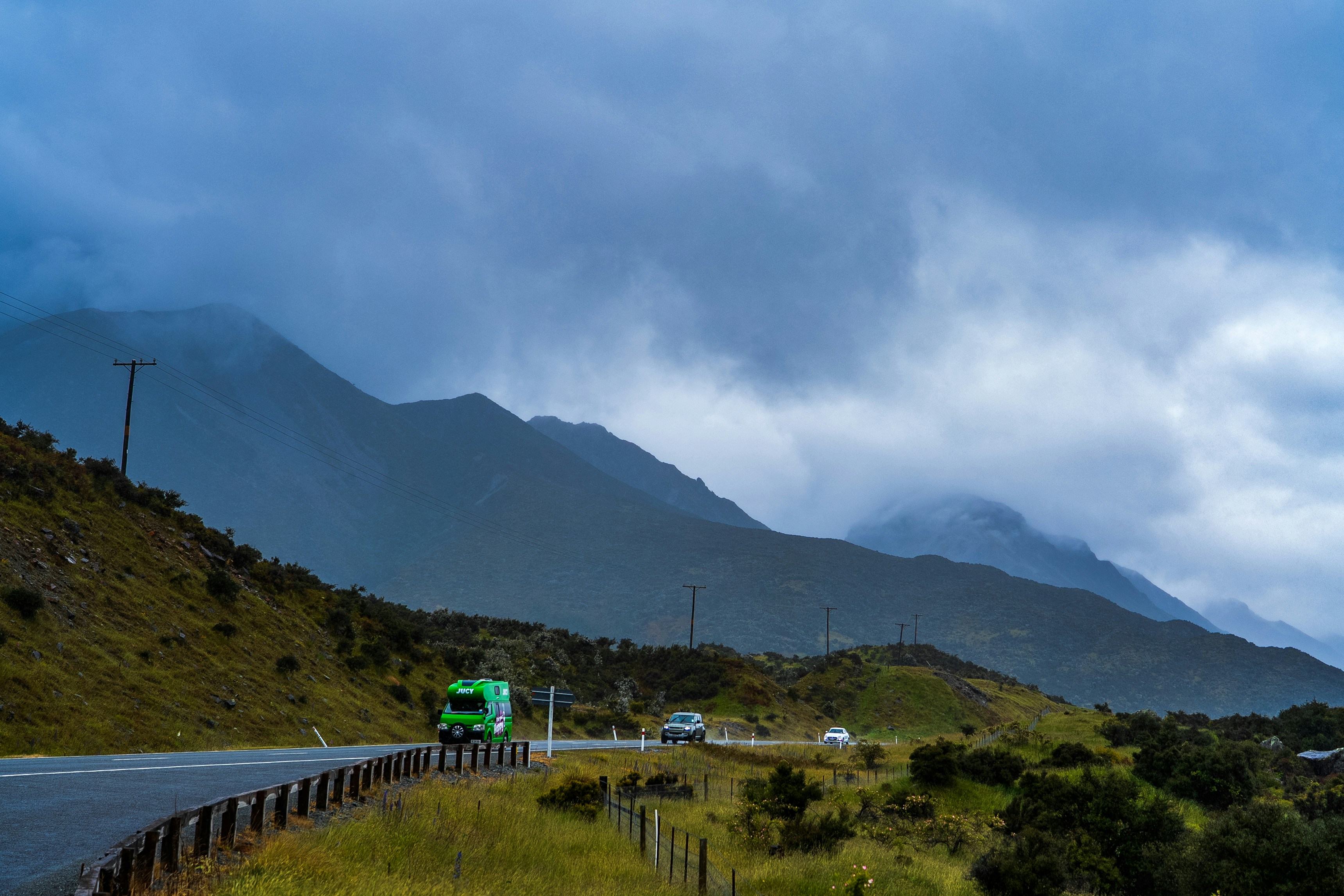A road winds past mountains under cloudy skies.