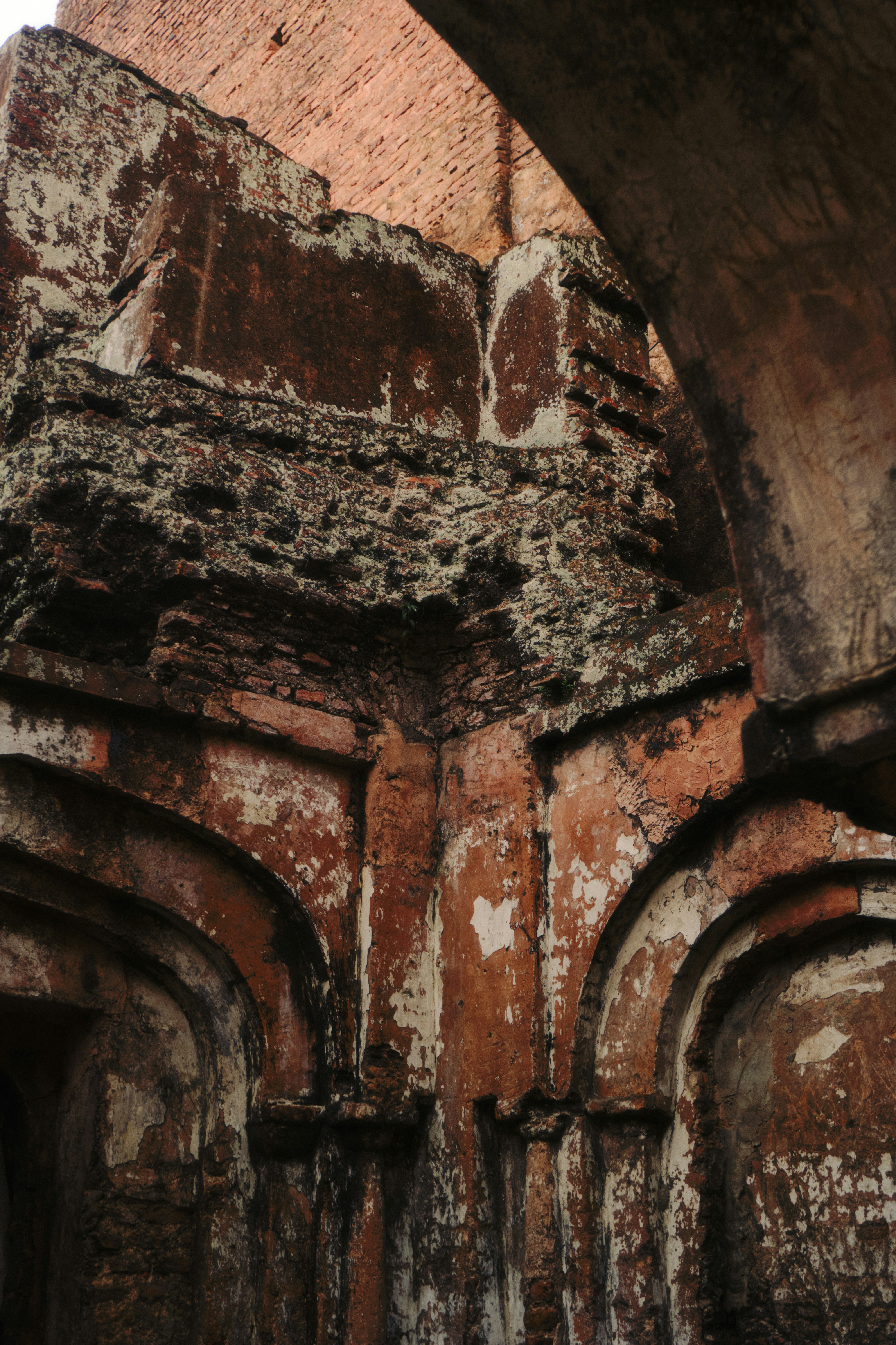 Intricate arches and weathered walls reveal the remnants of an ancient structure, adorned with moss and peeling paint.