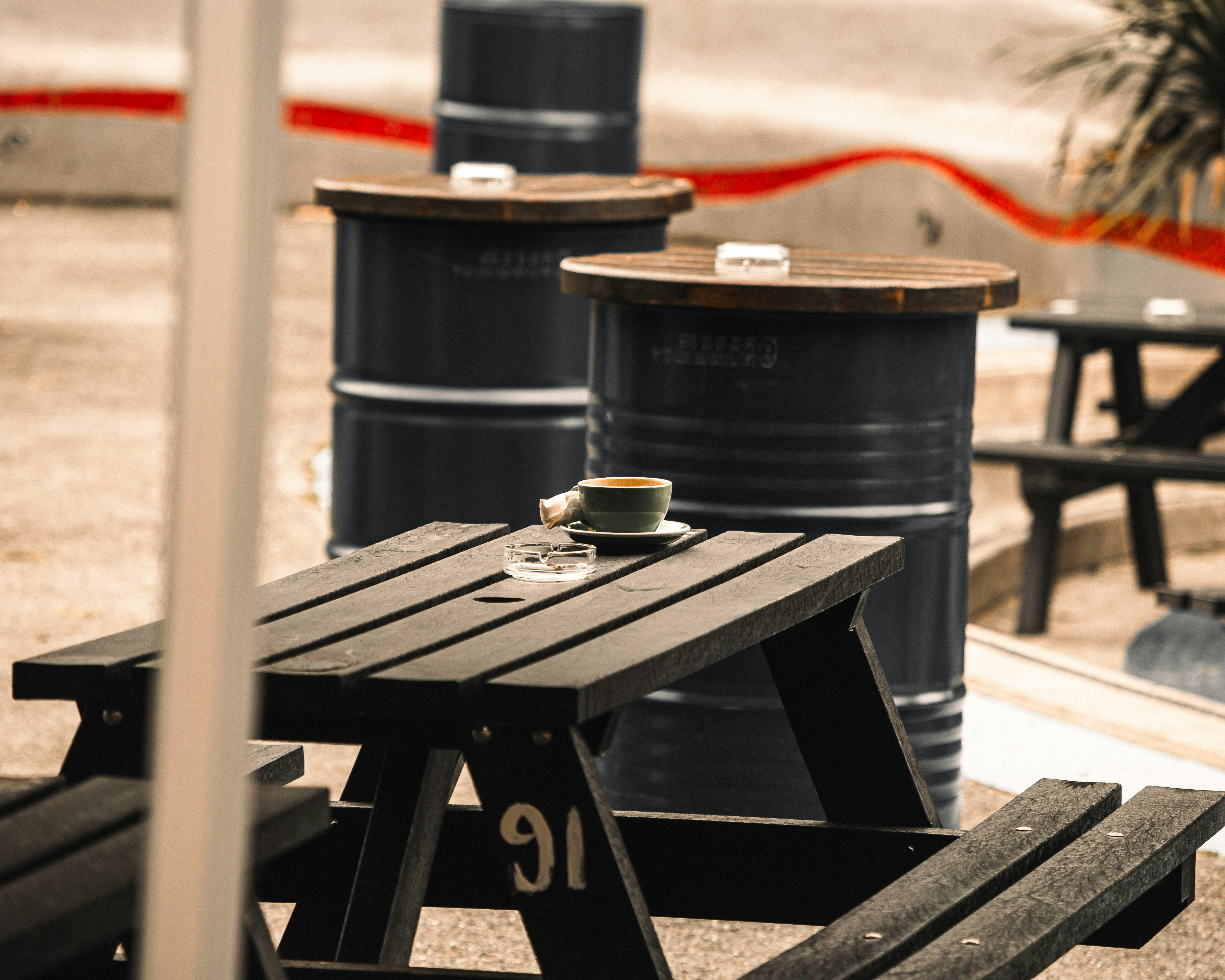 Teacup in the Quiet Gap: Weathered Wood Meets Industrial Blue Barrels