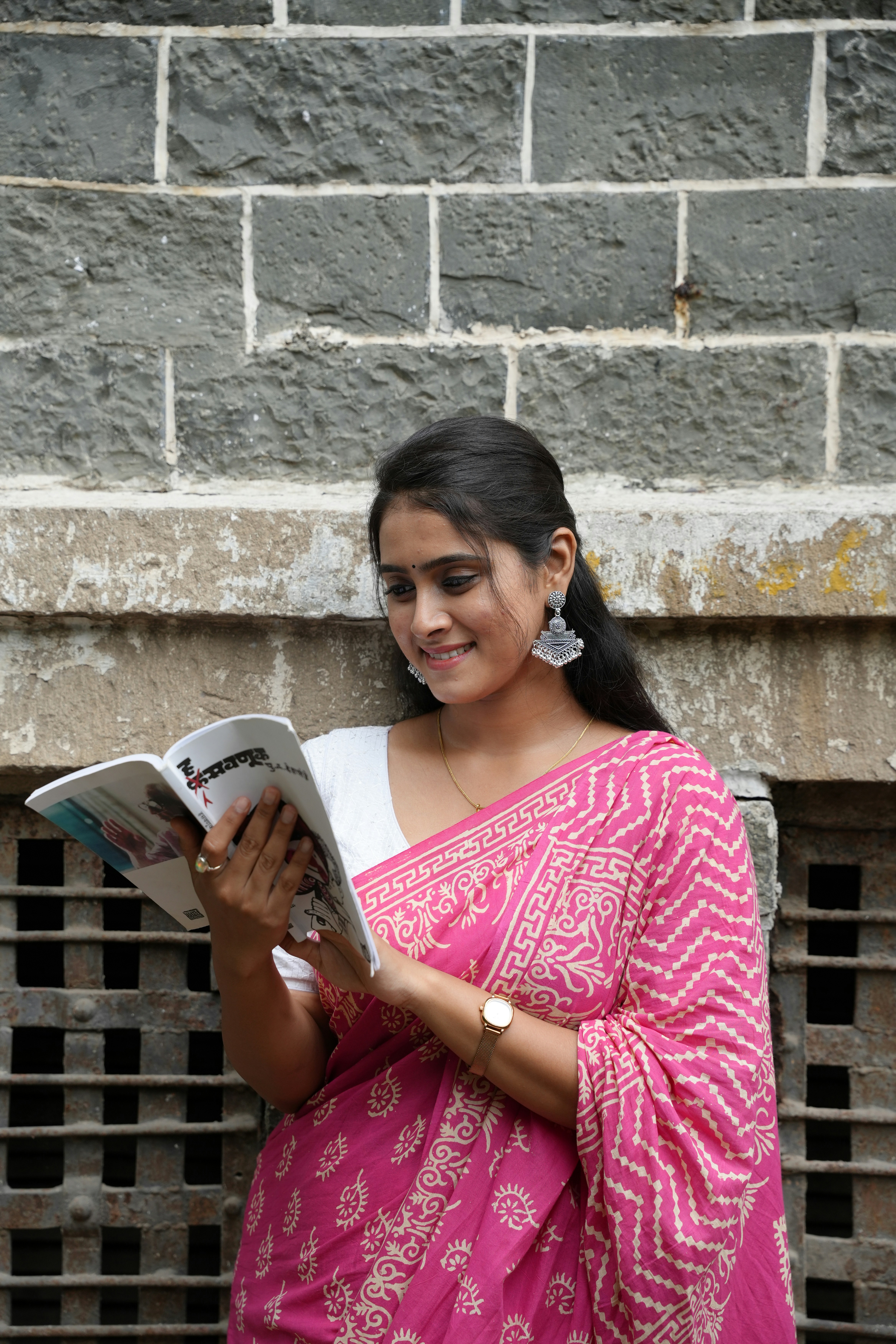 Woman reads a book while leaning against a wall.