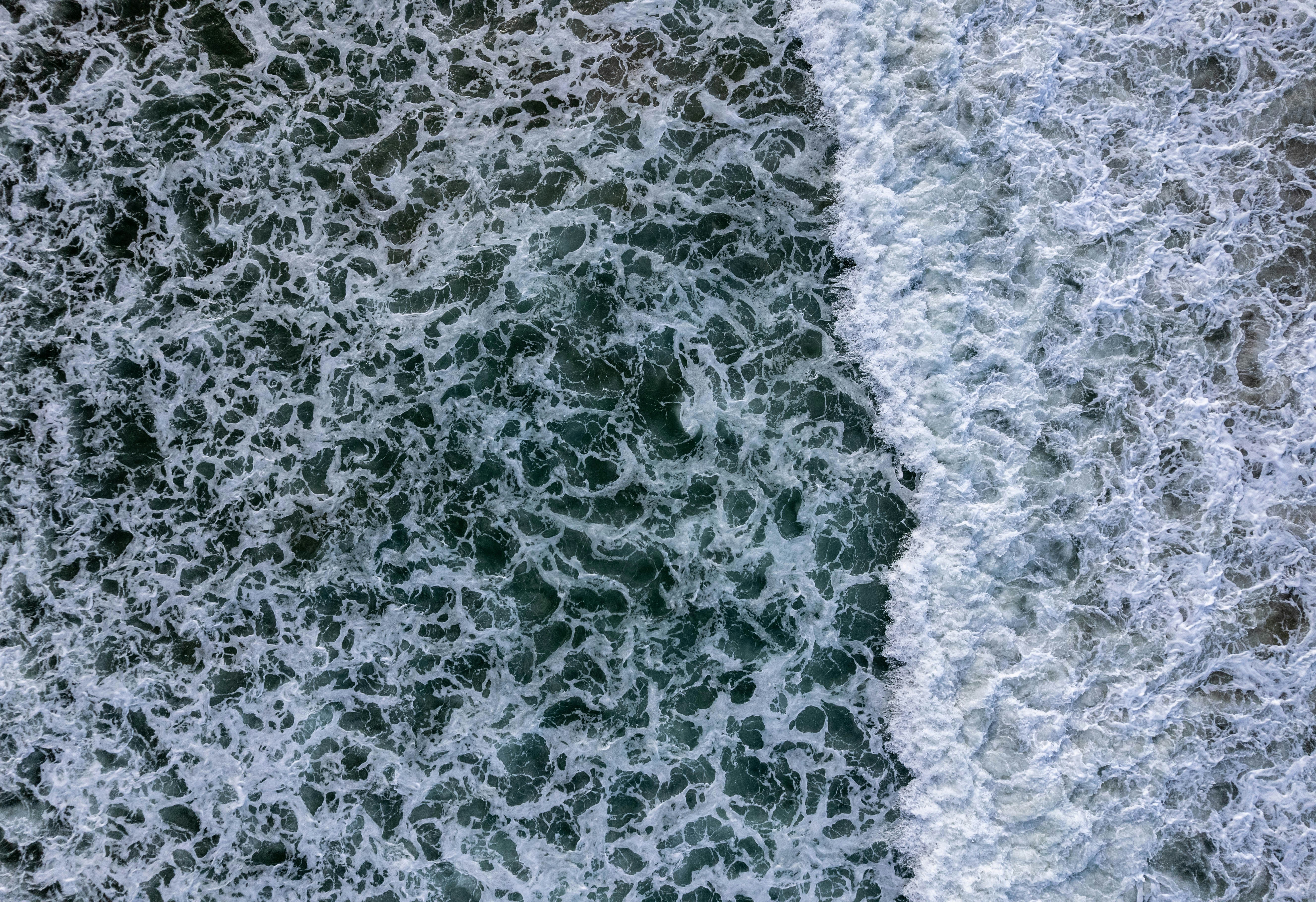 Waves crashing on the shore from an aerial perspective.