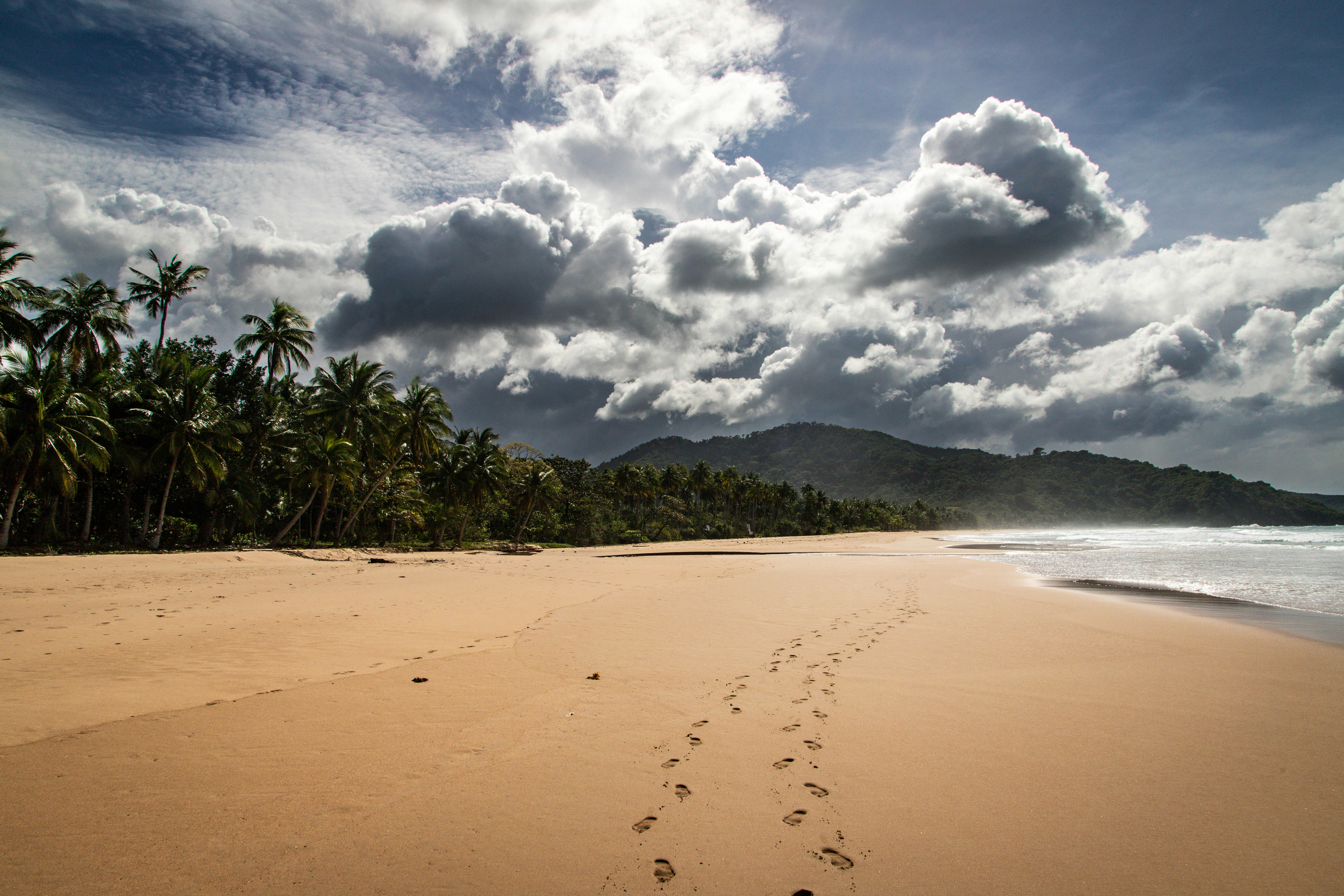Footsteps Toward the Horizon: A Quiet Tropic Beach Under Cloudy Sky