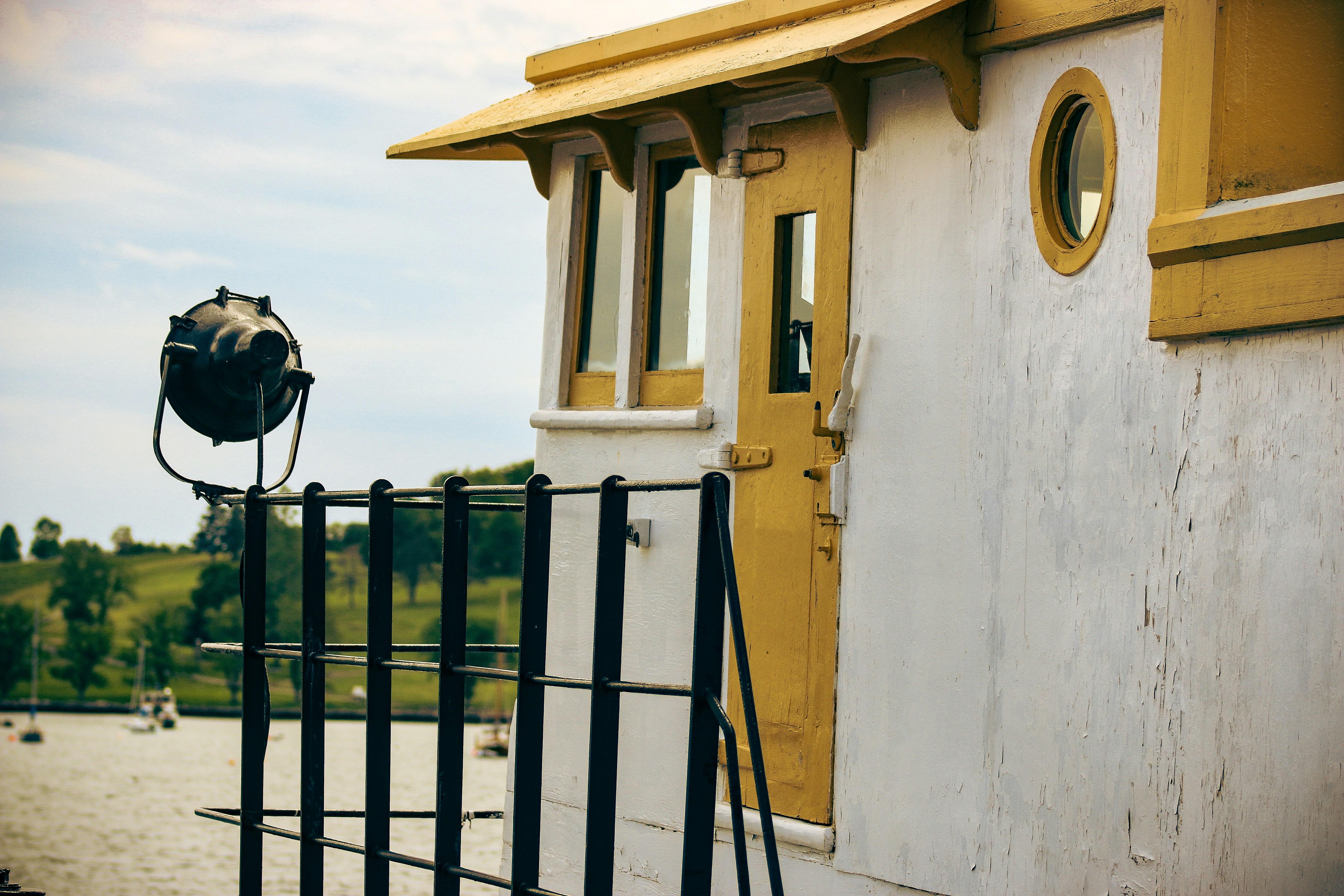 Close-up of a vintage boat cabin featuring a yellow door and a round window, set against a tranquil riverside backdrop.