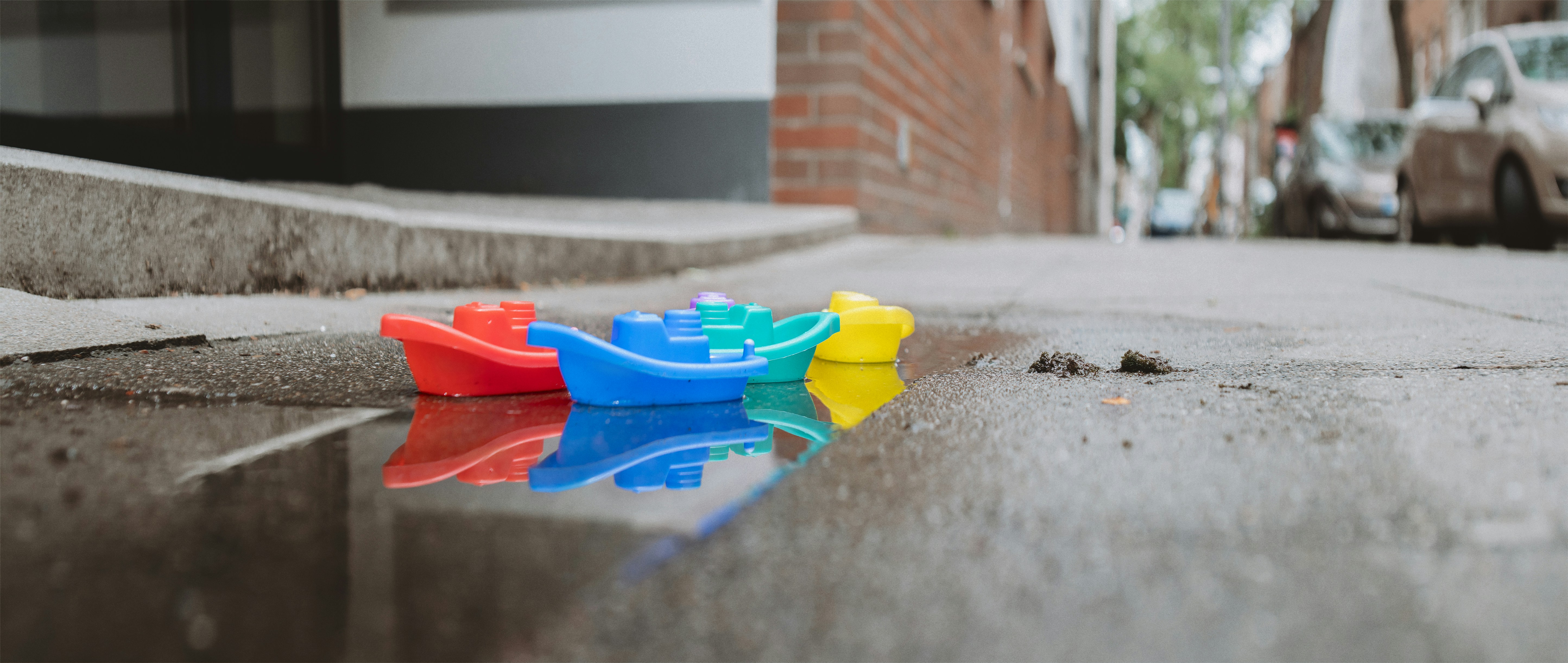 Colorful toy boats float in a puddle.