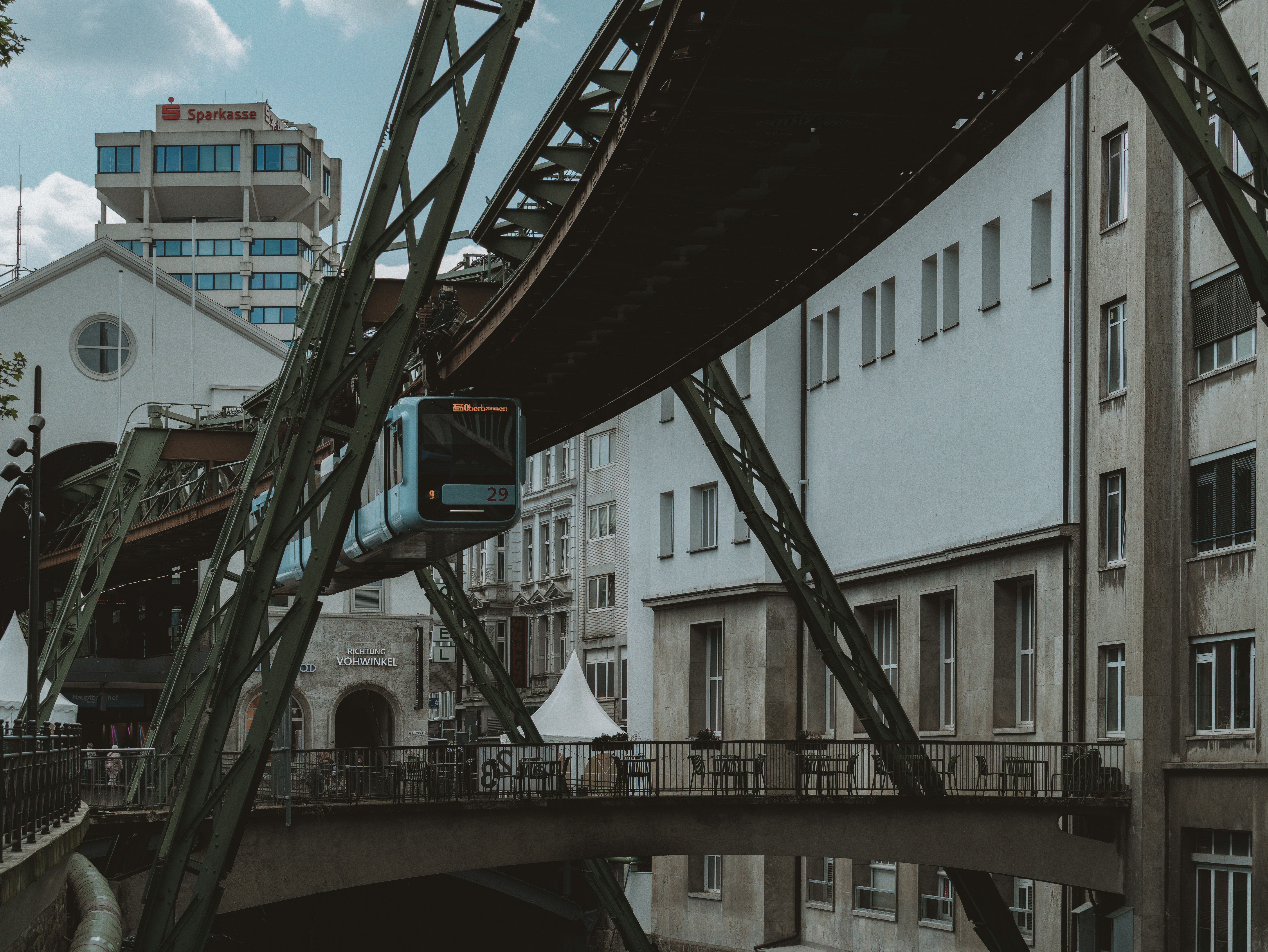 Monorail gliding above a modern cityscape, juxtaposed against historic buildings and a cloudy sky.