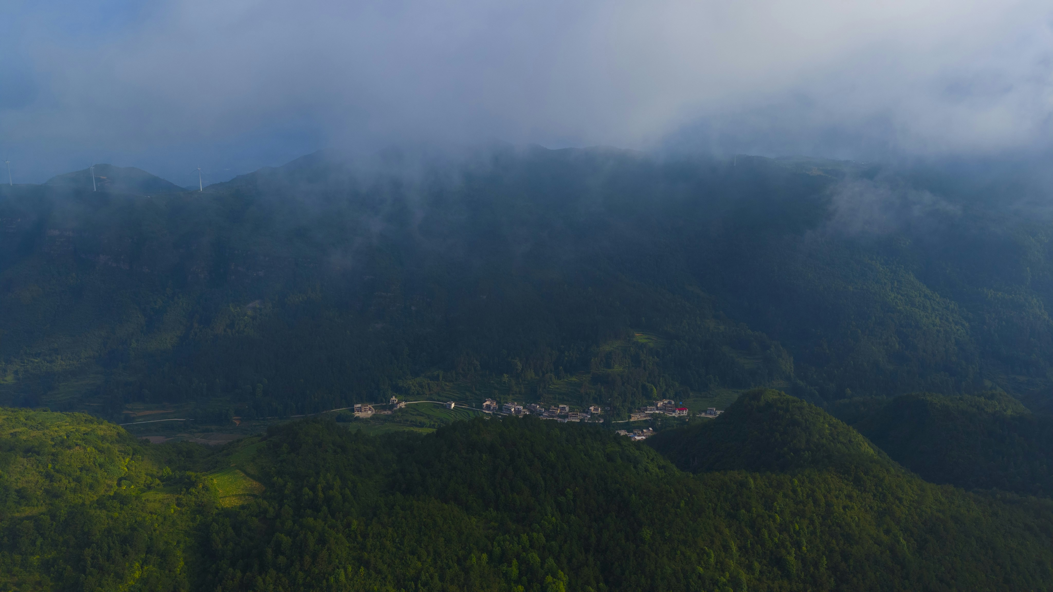 Aerial view of a secluded village nestled among lush green mountains, shrouded in mist and mystery.