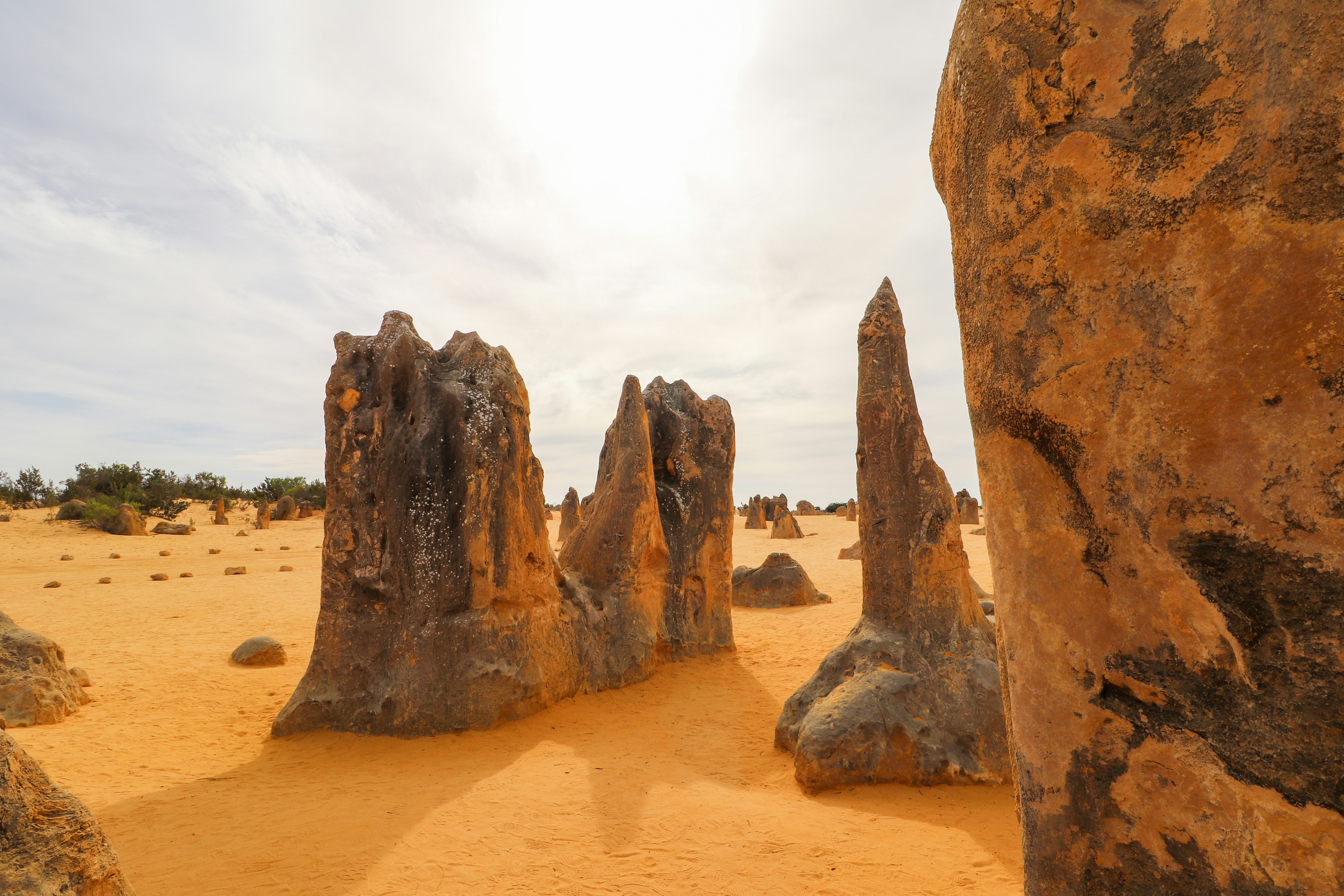 Unique rock formations rise from the golden sands, creating a surreal landscape under a soft, cloudy sky.