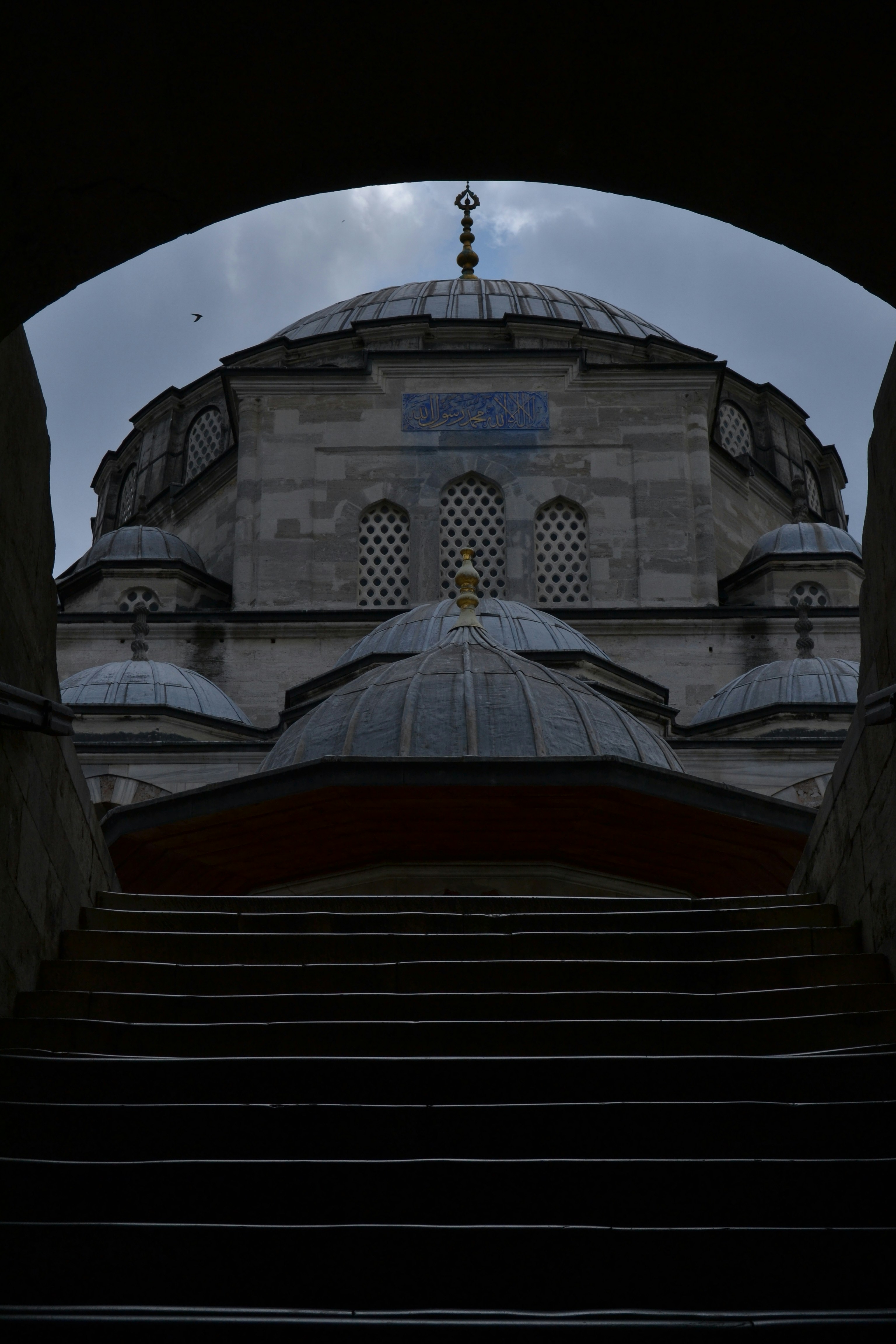 Silhouette of a grand mosque dome framed by an archway, highlighting intricate architectural details against a moody sky.