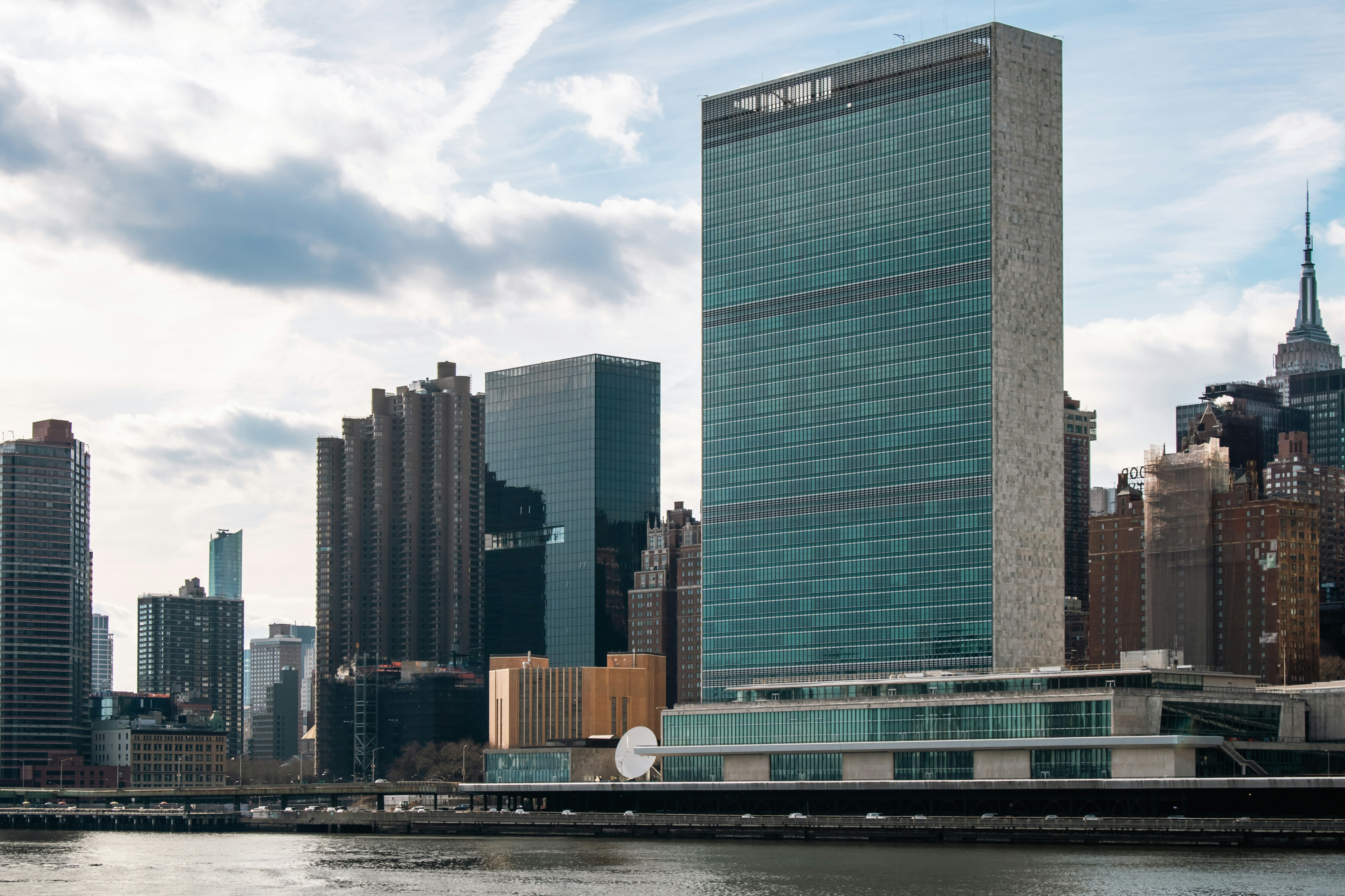 The United Nations building stands prominently along the river, surrounded by a diverse skyline of modern architecture. A blend of glass and concrete structures reflects the dynamic spirit of the city.