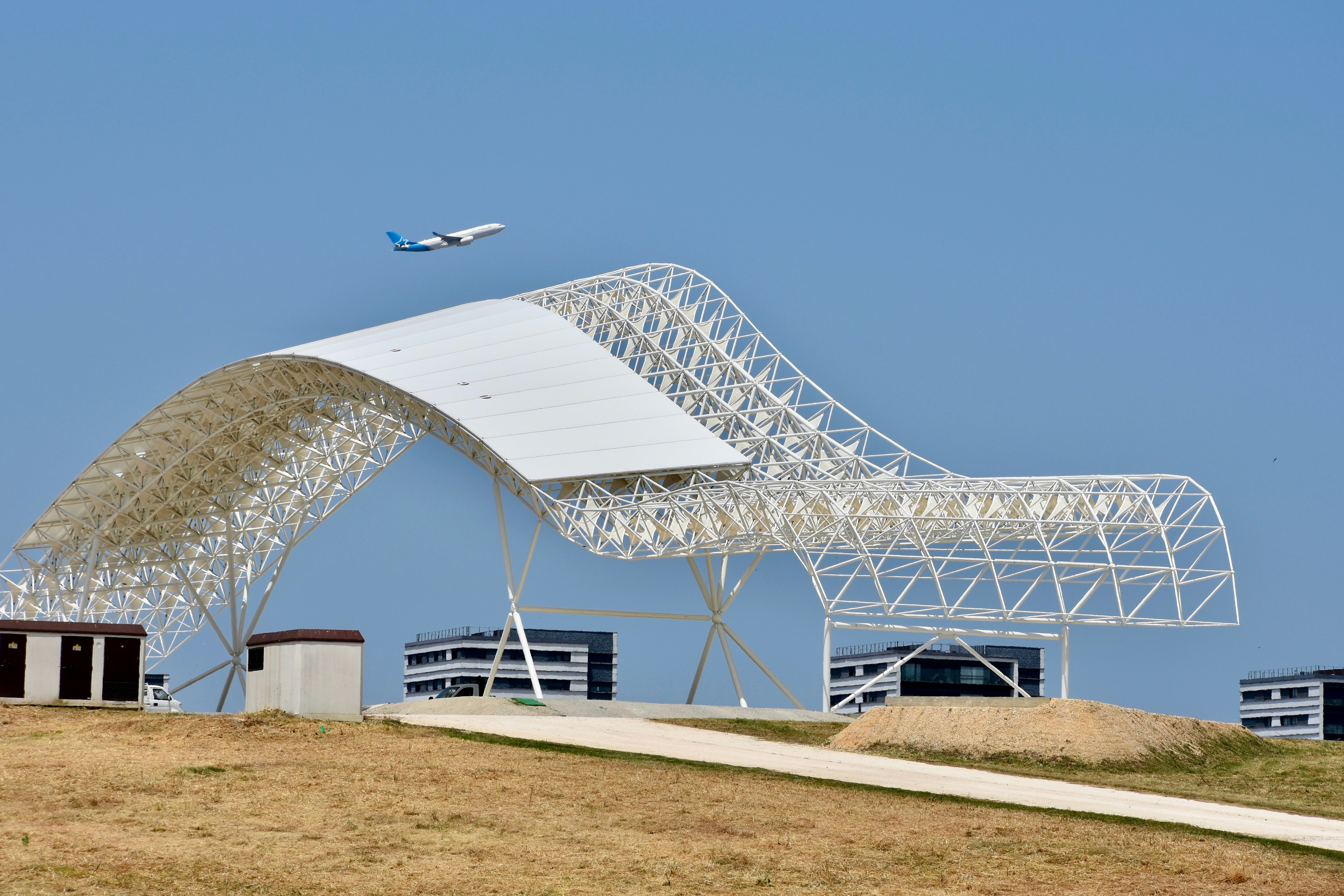 An airplane flies over a modern architectural structure. photo – Free ...