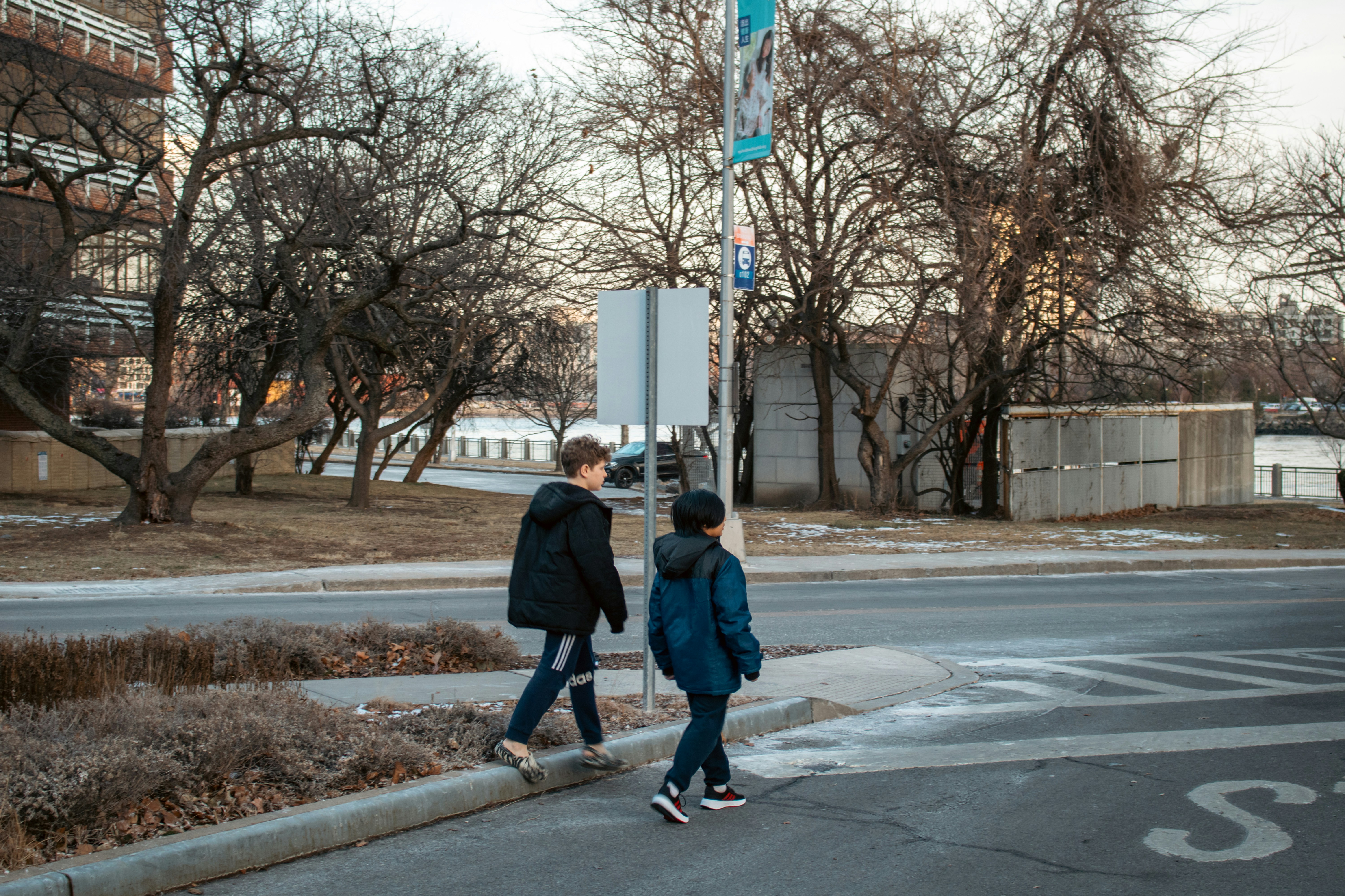 Two children walking along a city street, surrounded by bare trees and urban architecture. The scene captures a moment of exploration in a tranquil environment.