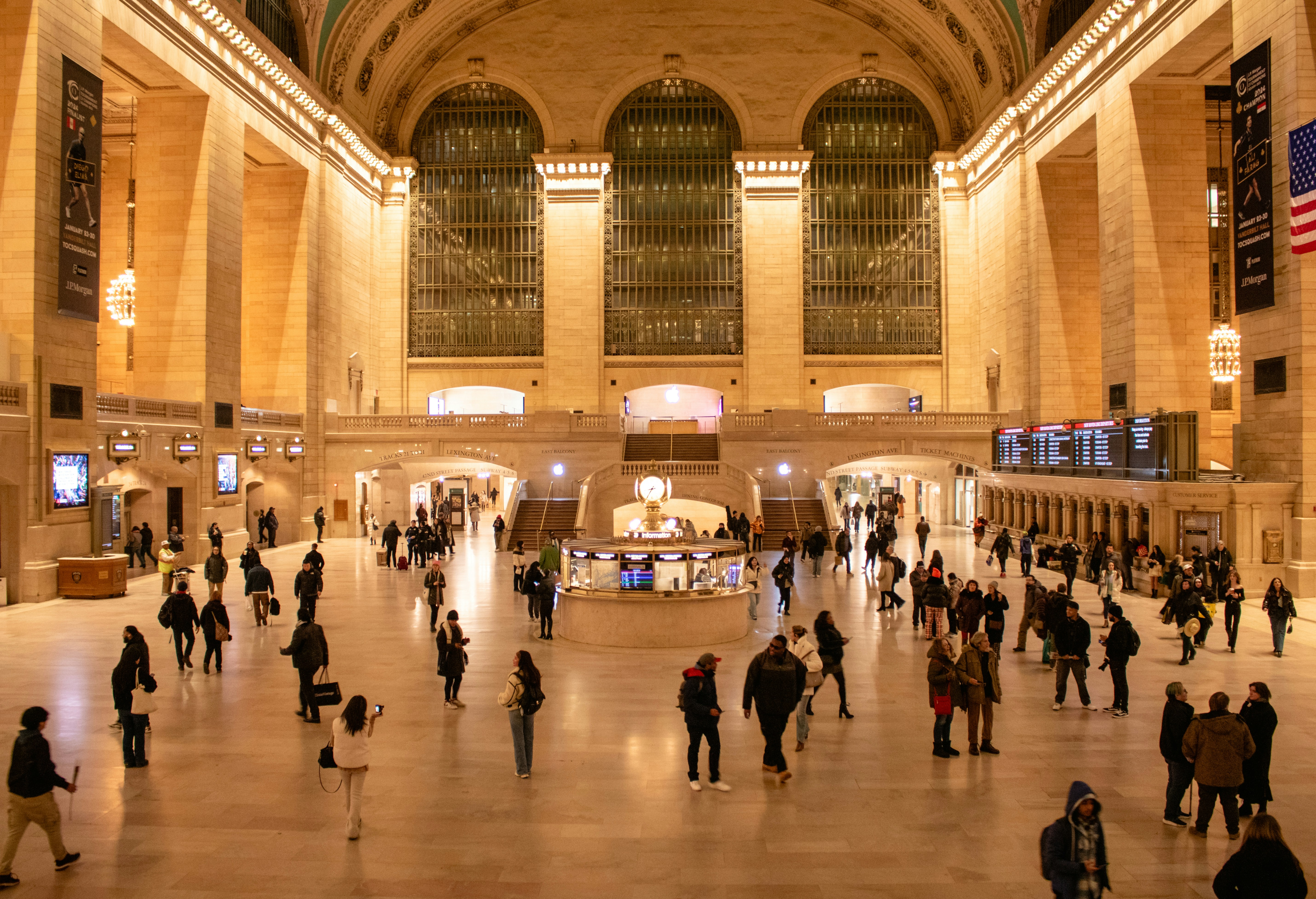 Grand Central Terminal, often called Grand Central Station, is a historic commuter rail terminal in Midtown Manhattan, New York City. It's a transportation hub, architectural marvel, and a symbol of the city's resilience. It's known for its Beaux-Arts design, including the celestial ceiling in the Main Concourse and the iconic four-faced clock. The terminal serves as the southern terminus for the Metro-North Railroad's Harlem, Hudson, and New Haven lines. | People walk through the spacious grand central terminal.