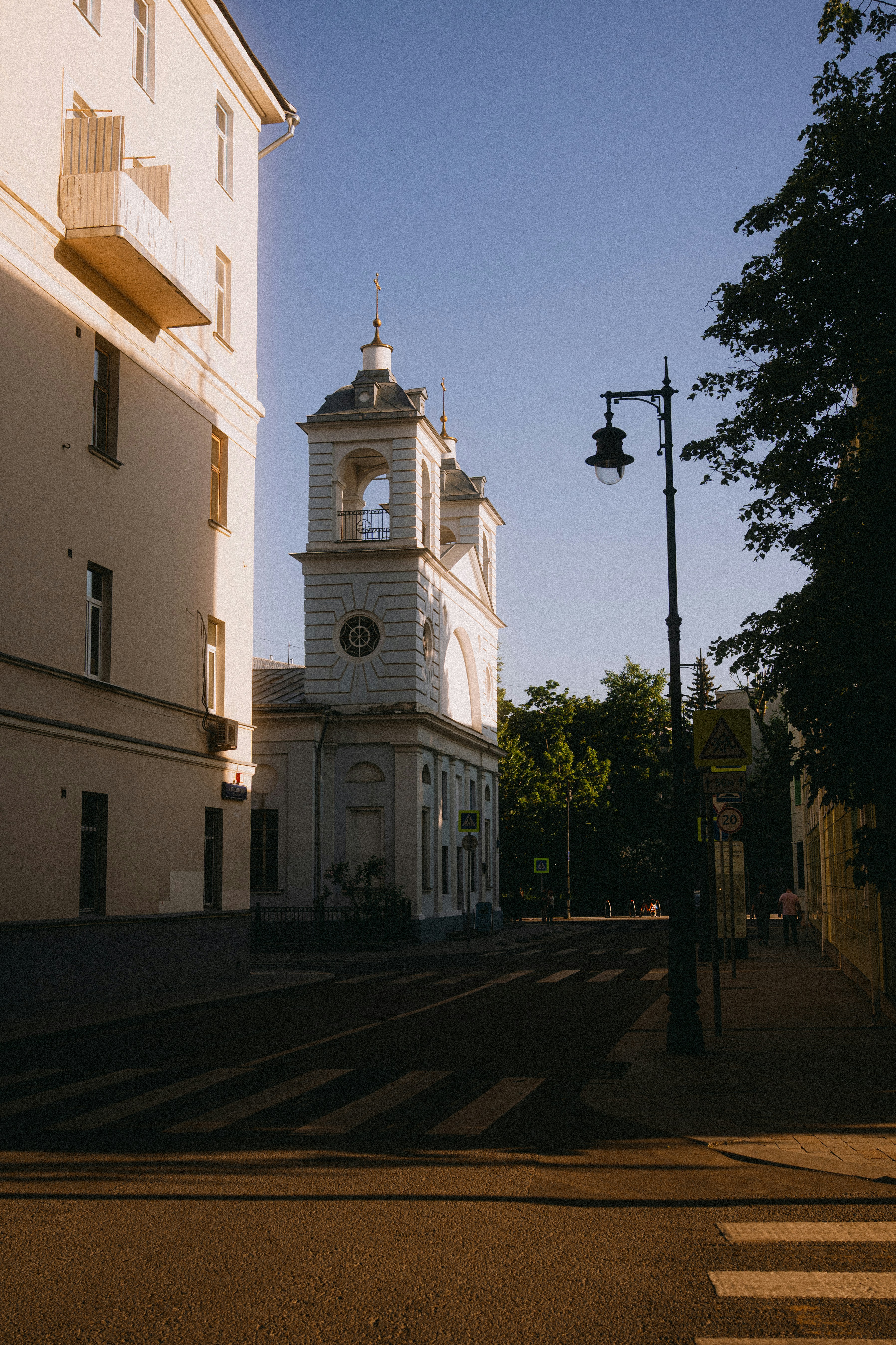 A church sits on a street bathed in sunlight.