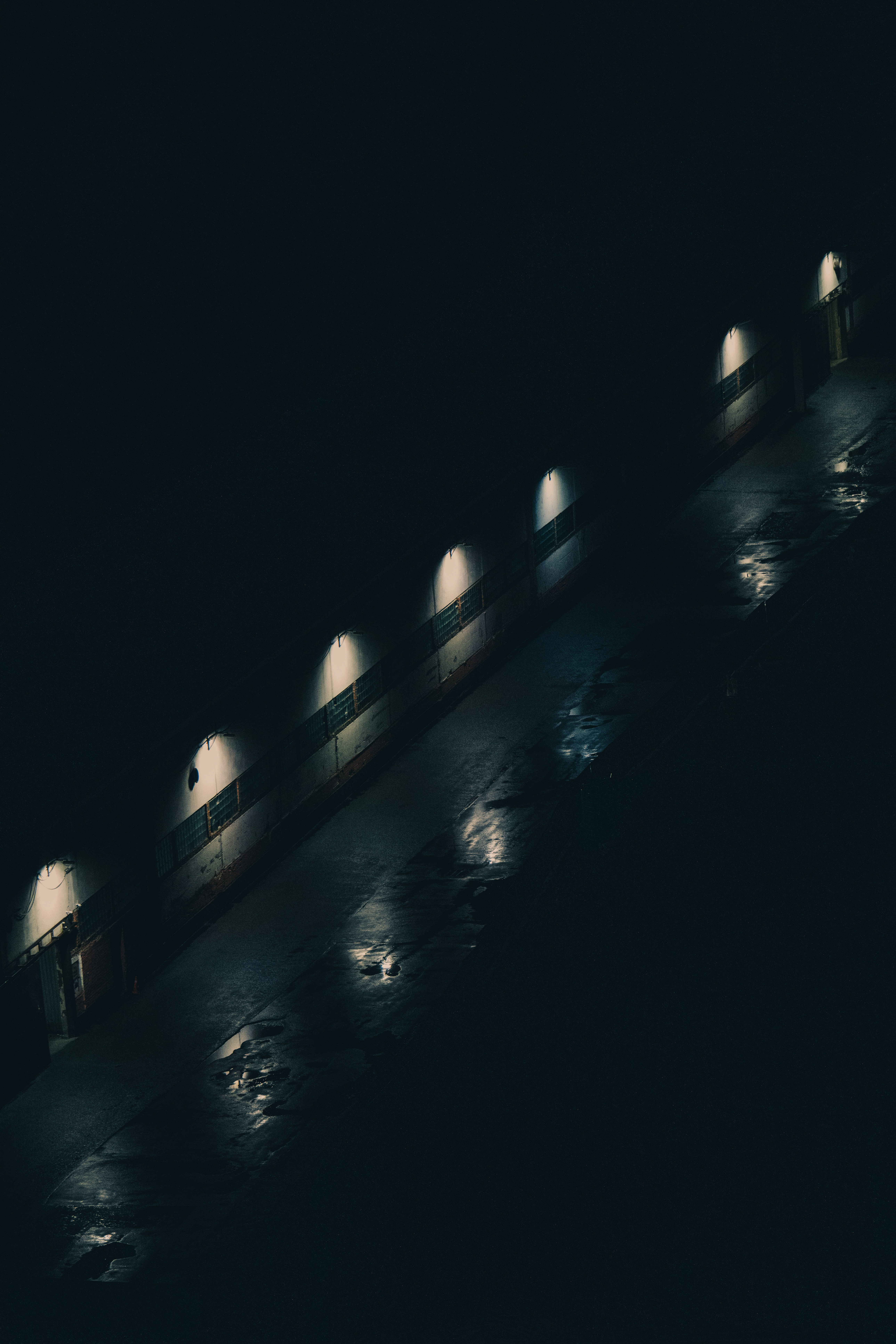 A lone figure stands on a wet, lit street.