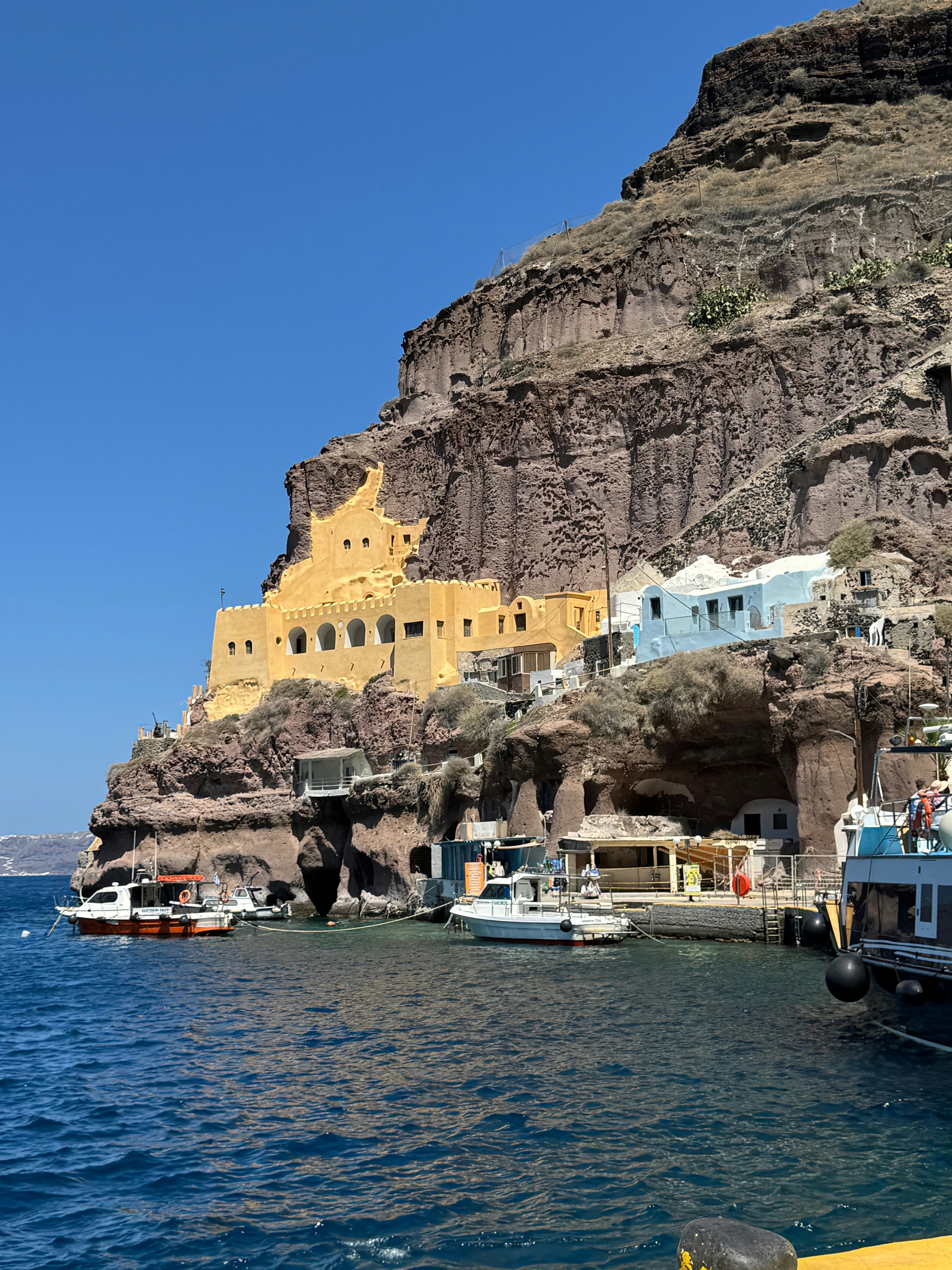 Vibrant yellow building perched on rocky cliffs alongside a serene harbor filled with boats, showcasing the beauty of coastal architecture.