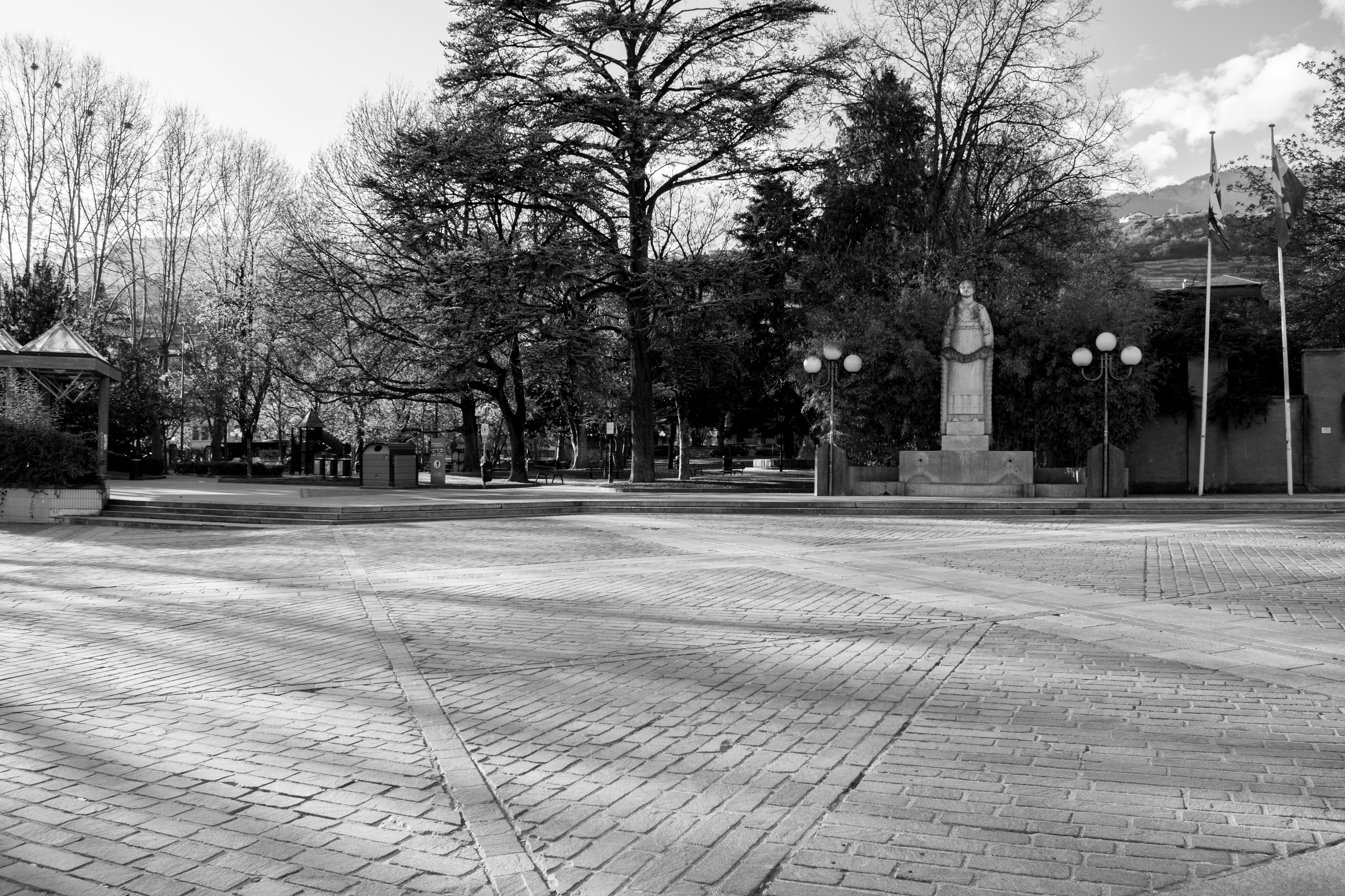 A park features trees, a statue, and a brick ground.