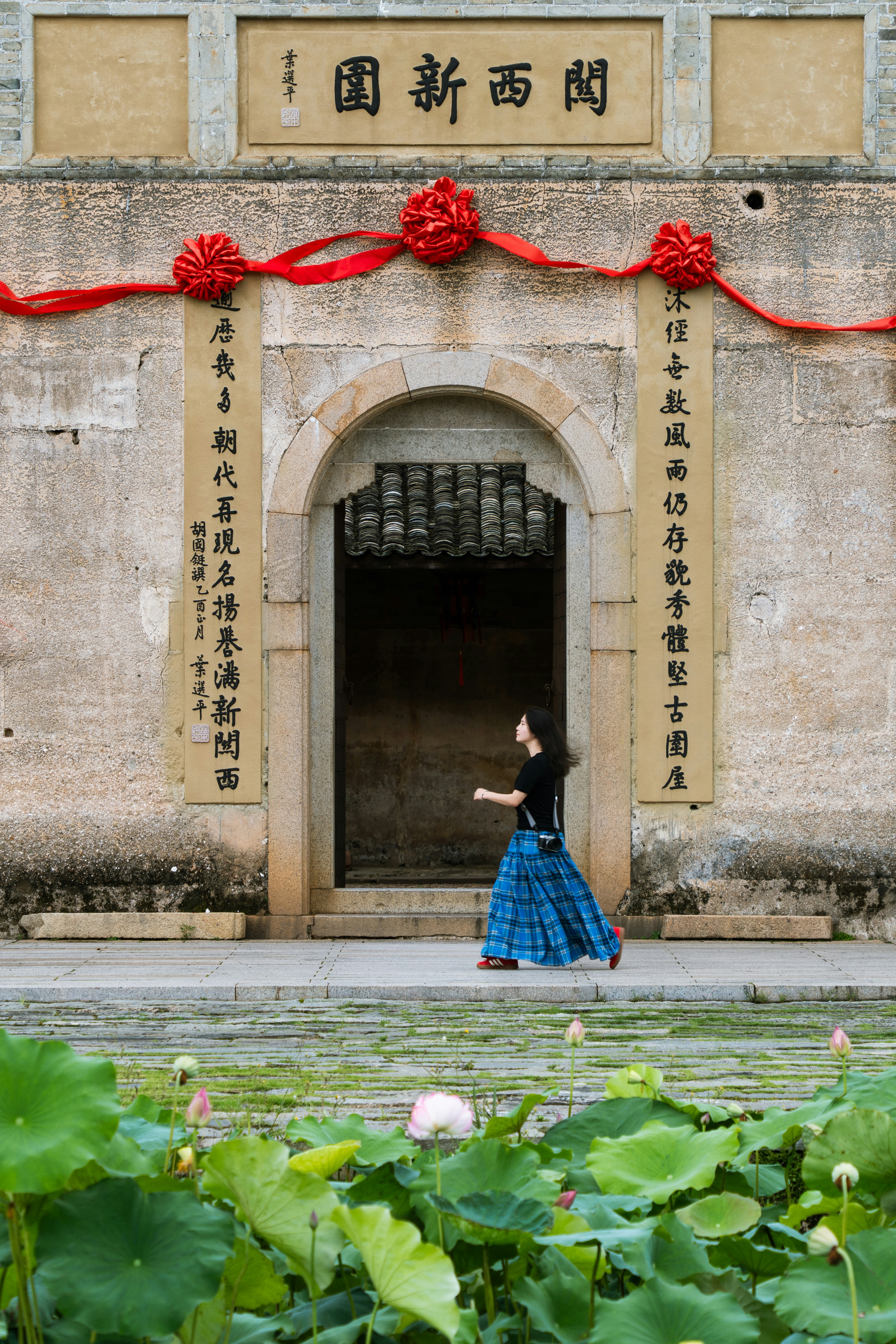 Red Ribbon Gate: A Woman Walks Through Time-Worn Courtyard