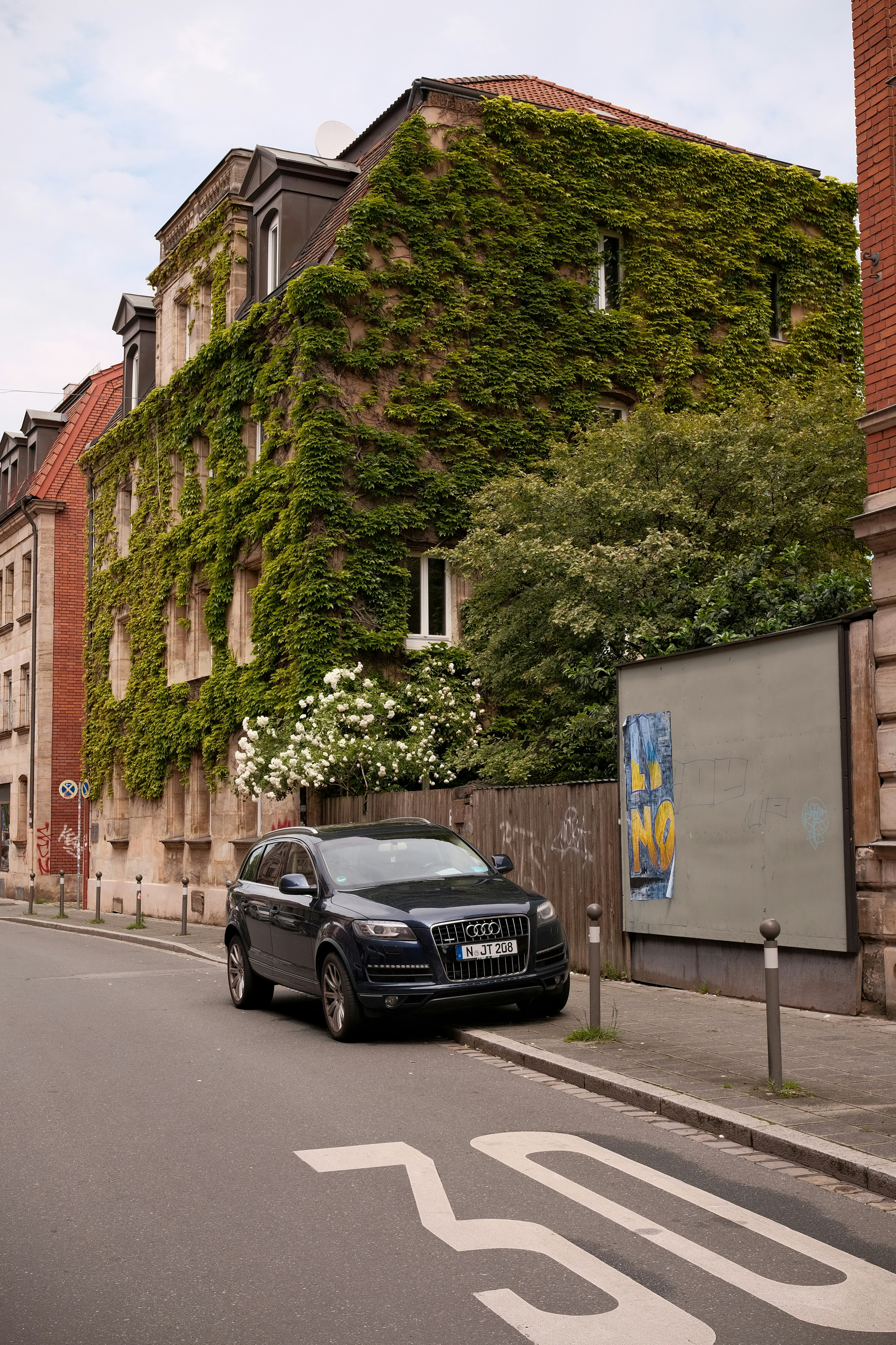 Audi Q7. Historic building covered in green ivy with a parked SUV on a quiet city street during the day | A car parks next to a building covered in vines.