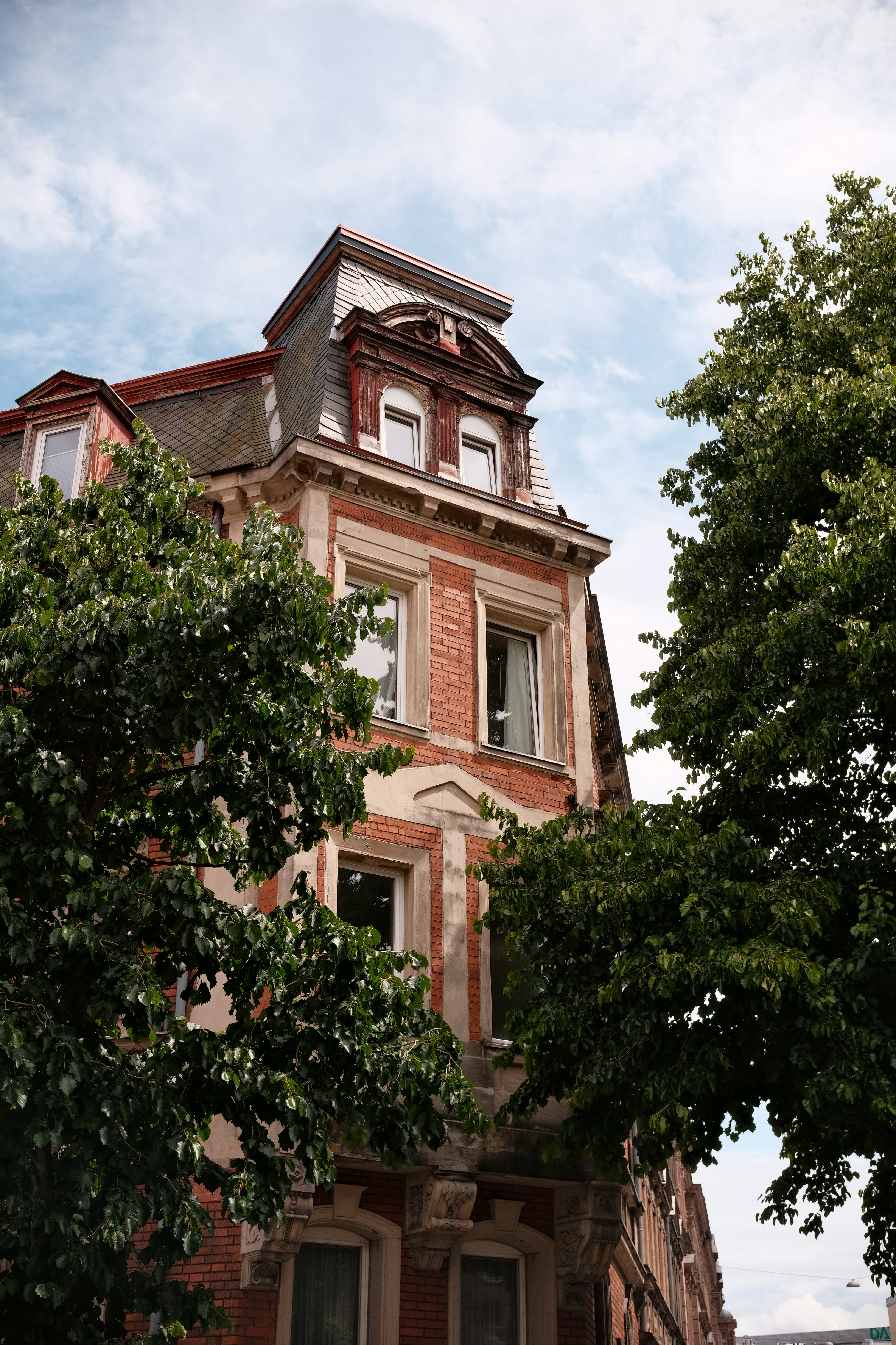 Historic brick building with wooden details surrounded by lush green trees on a sunny day in an urban neighborhood | A beautiful european building surrounded by trees.