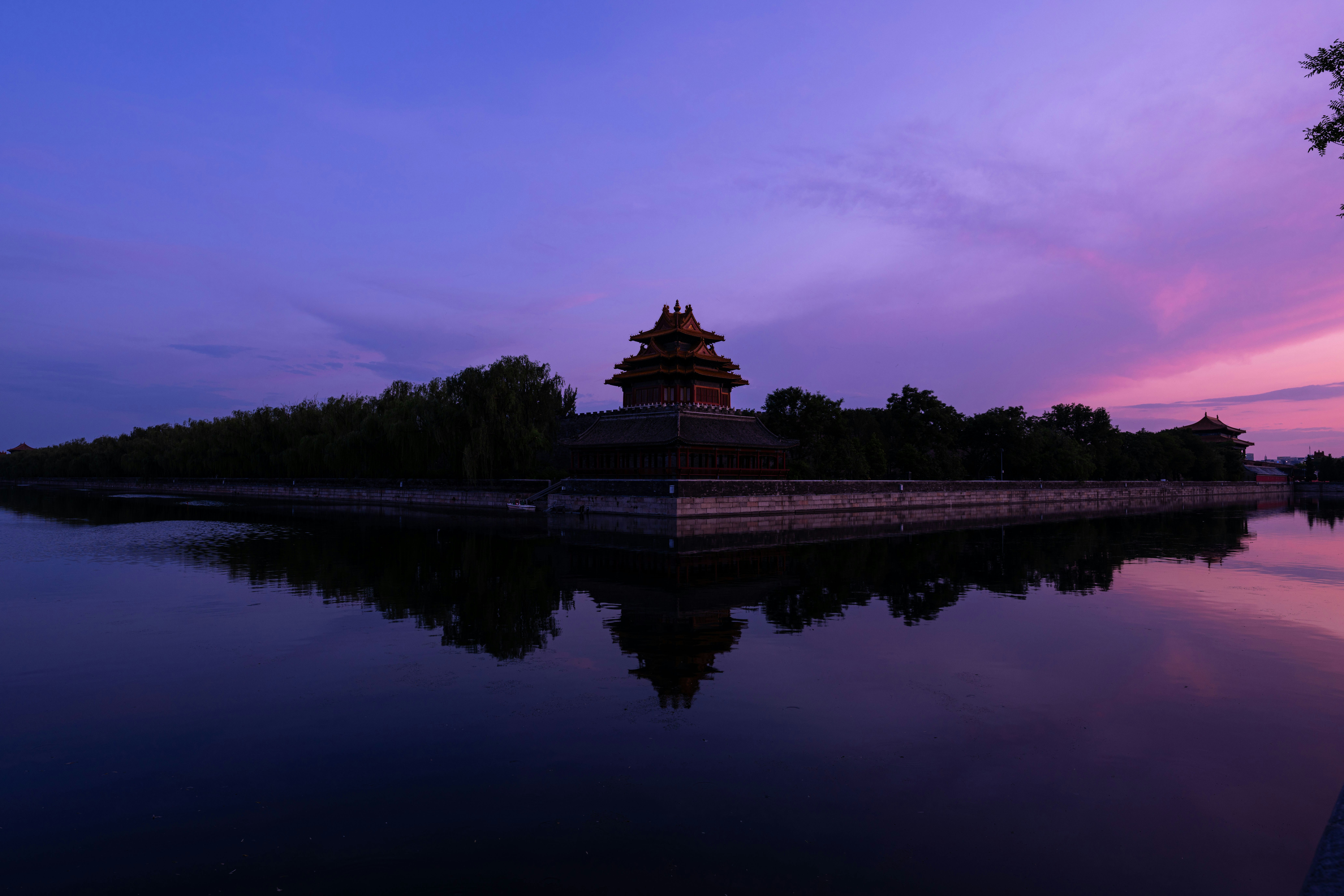 Historic pavilion illuminated by twilight, surrounded by calm waters reflecting a vibrant sky.