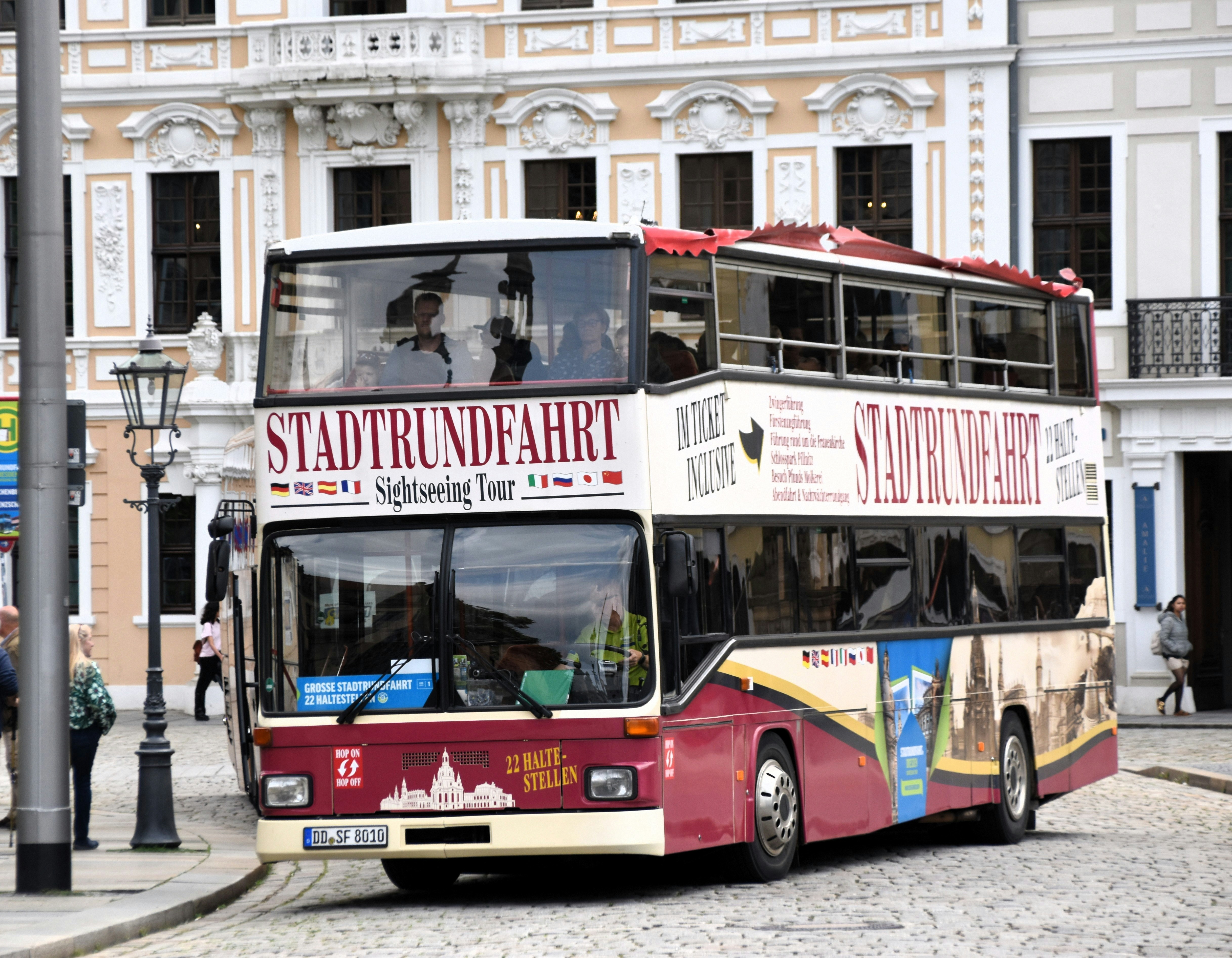 Double-decker sightseeing bus navigating through a historic city square, showcasing architectural details in the background.
