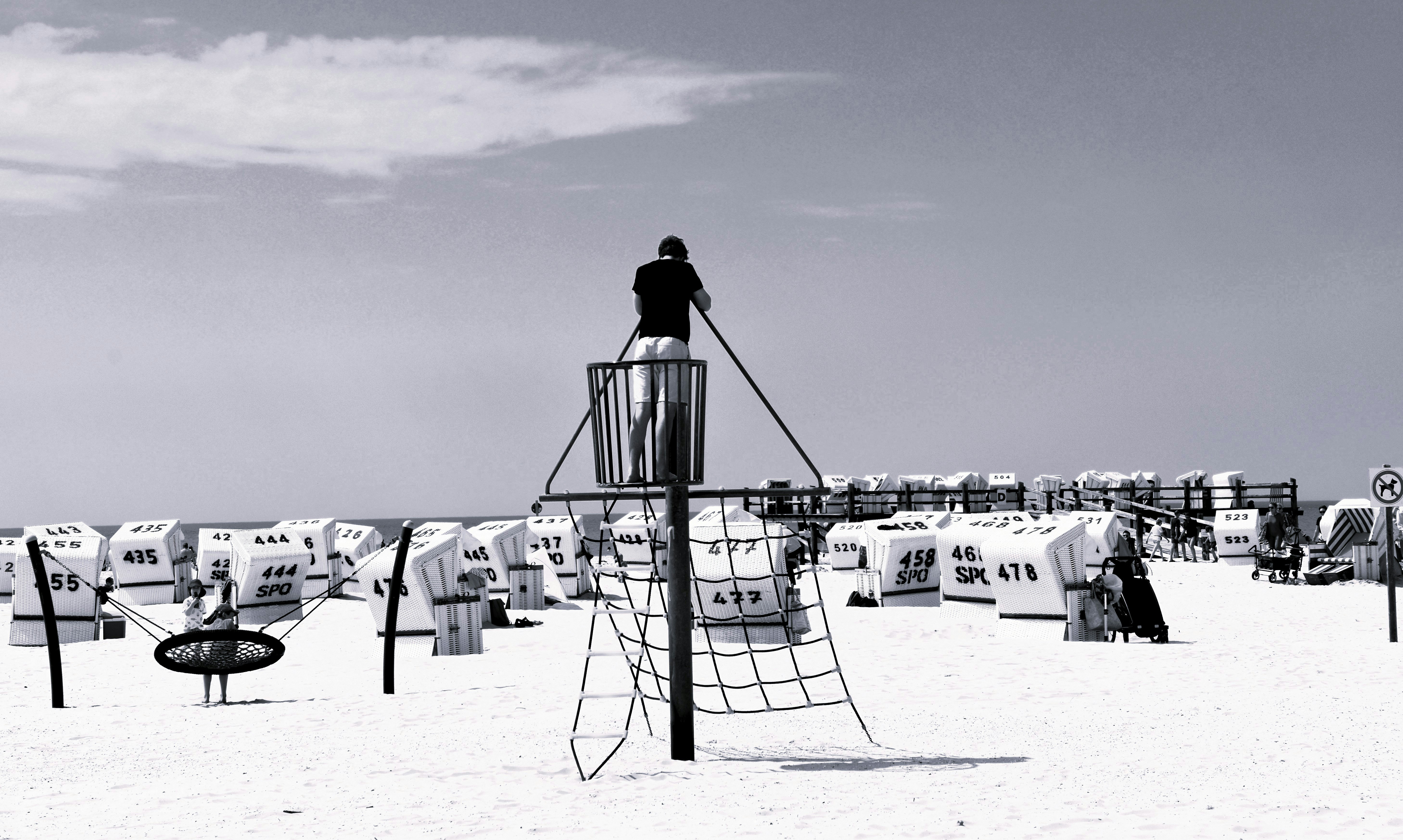 Lifeguard perched on a tower overseeing a beach dotted with numbered cabanas. The scene captures the essence of summer leisure and safety.