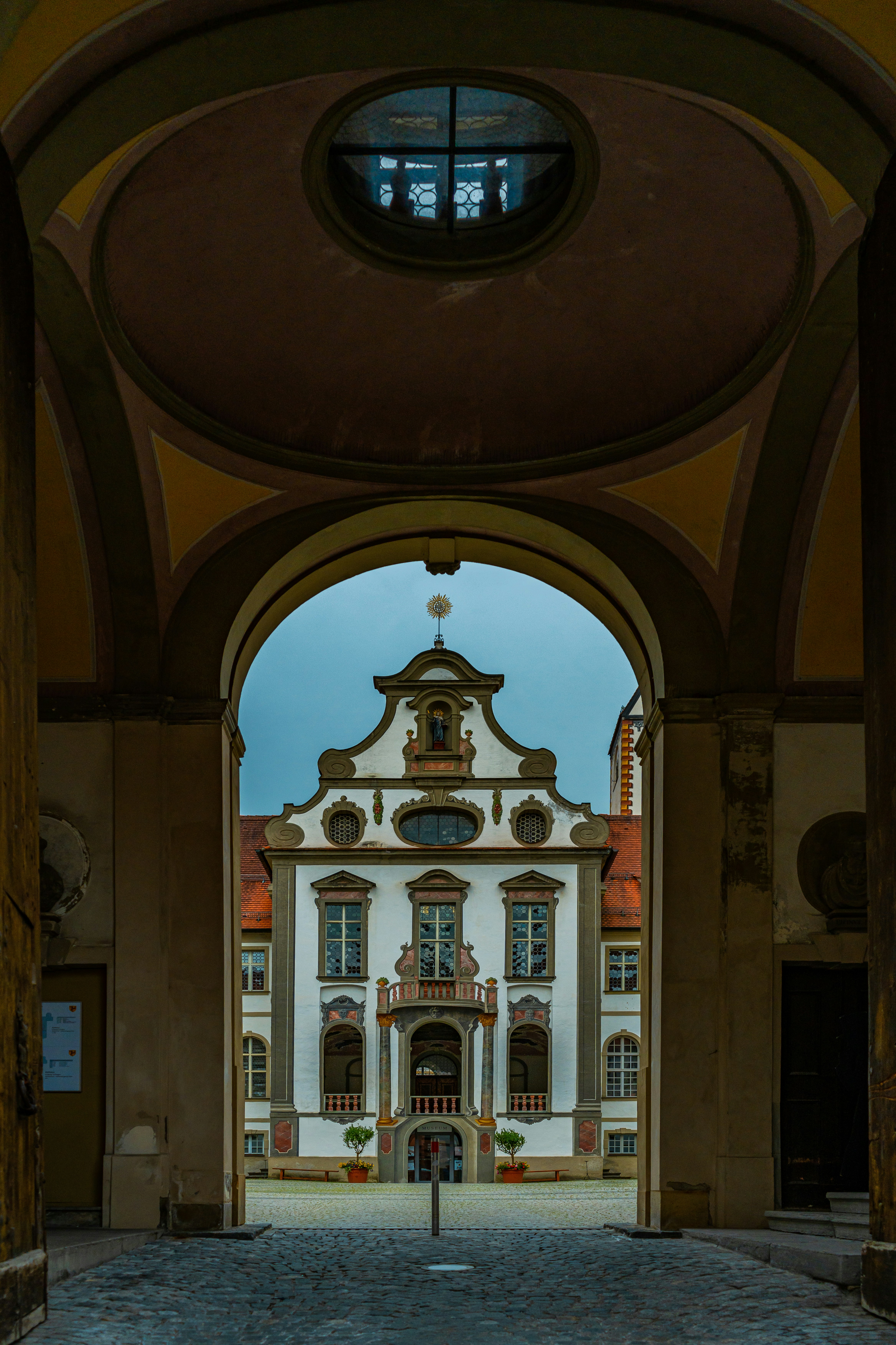 Baroque-style building framed by an ornate archway, showcasing intricate details and vibrant colors against a cloudy sky.