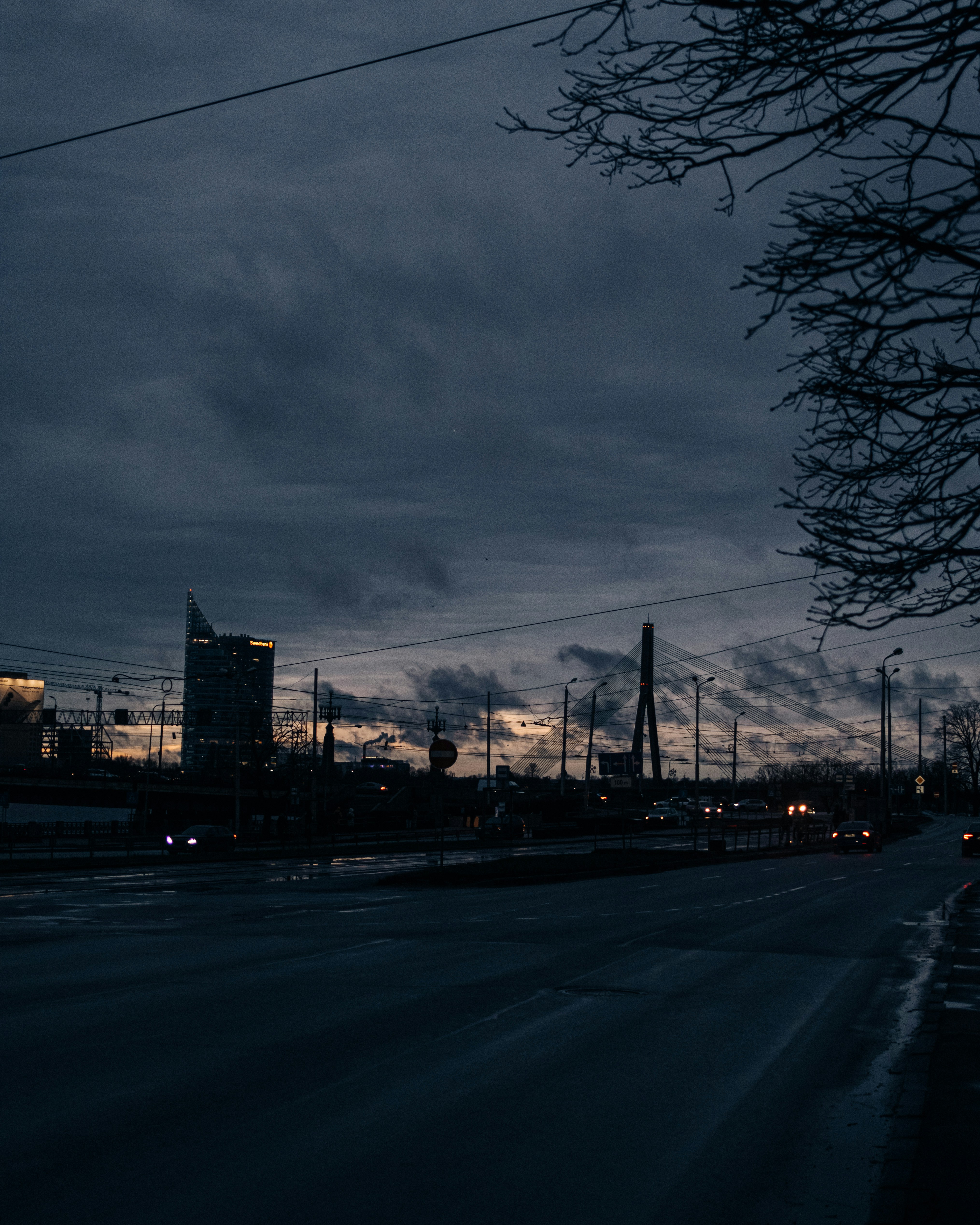 Silhouetted city skyline under a dramatic twilight sky, with illuminated buildings and a prominent tower amidst a quiet street.