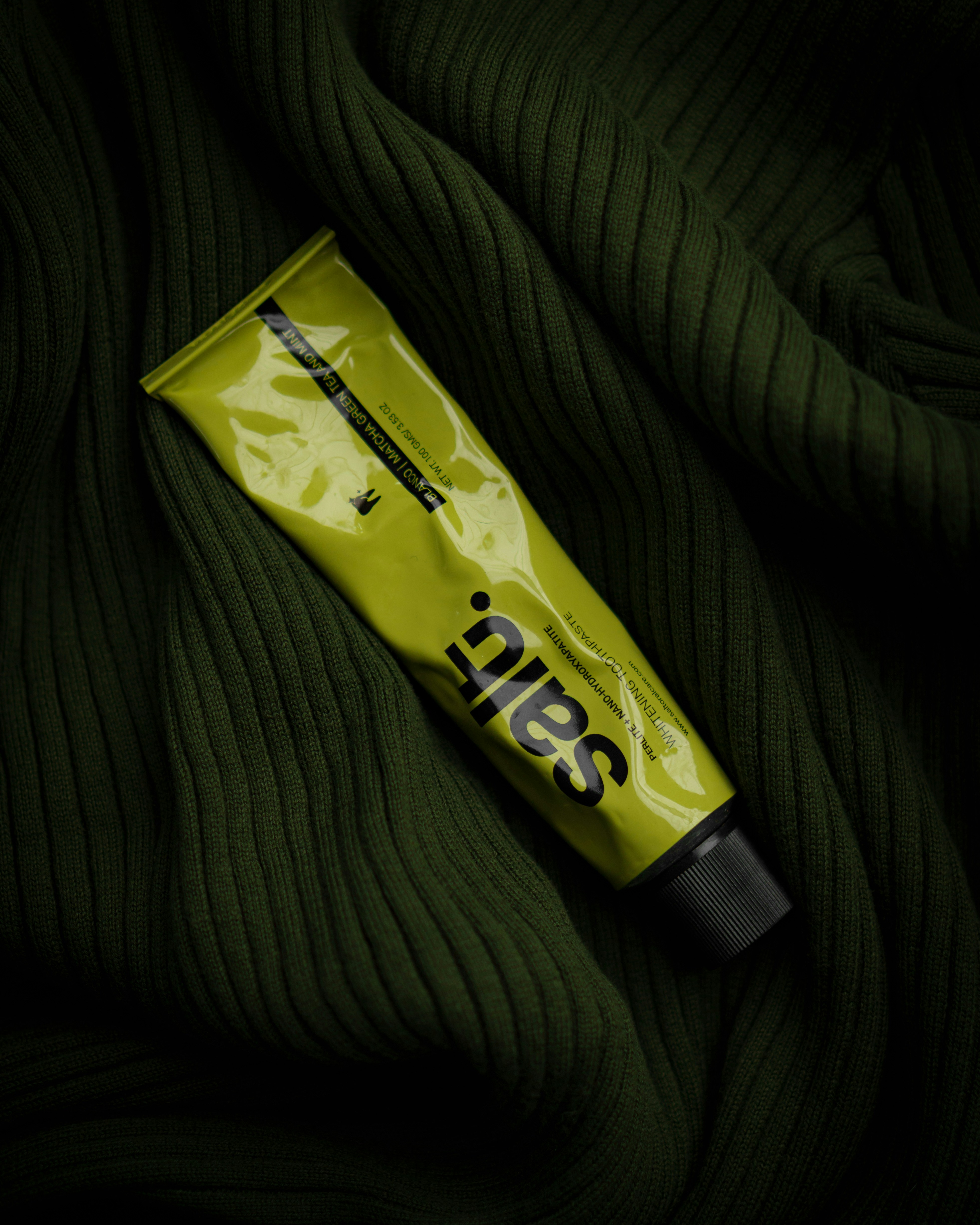 Product Photography of a green toothpaste bottle. | A tube of product lays on a dark fabric.